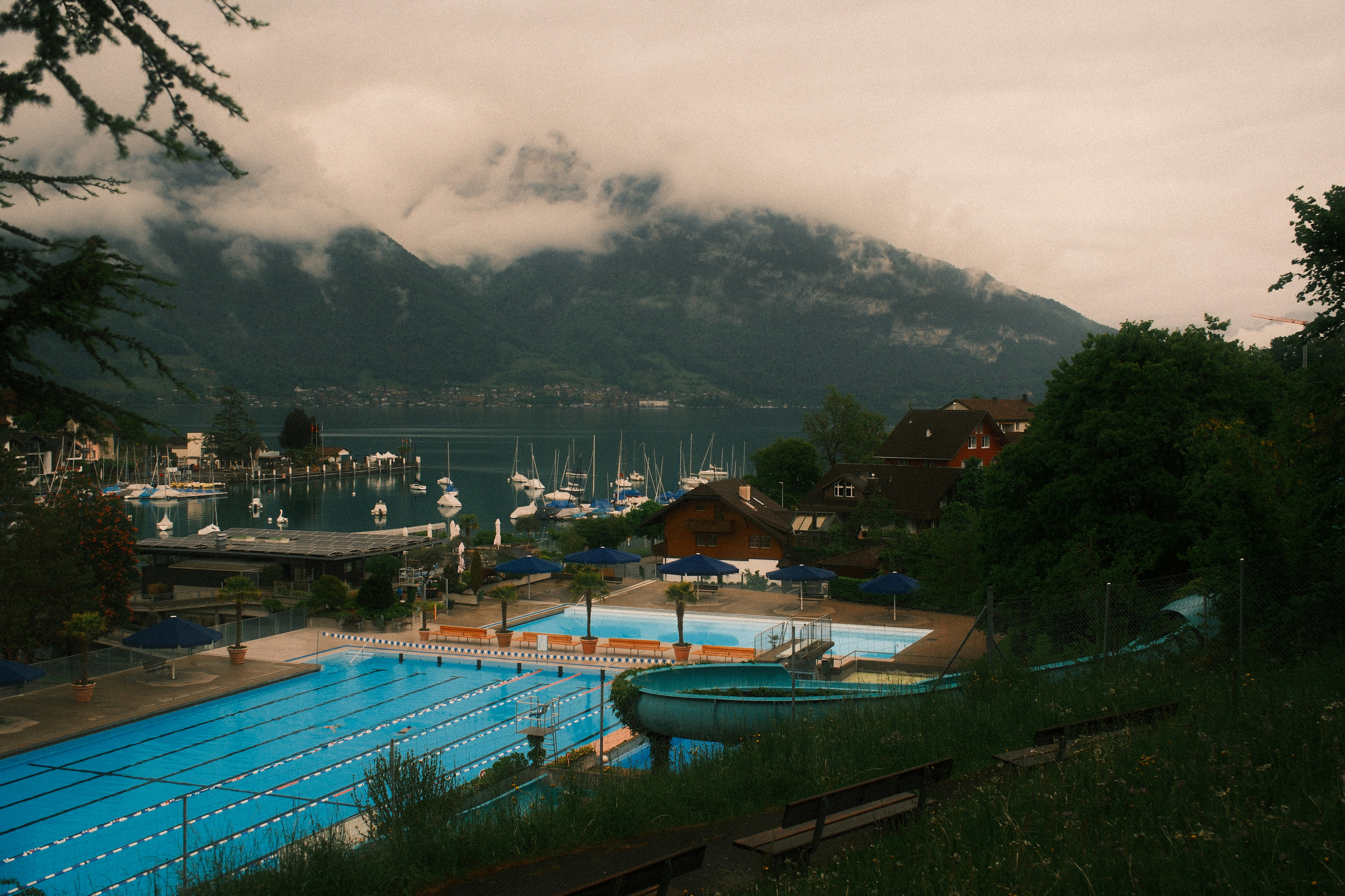 Swimming pools and a marina with mountains under cloudy sky.