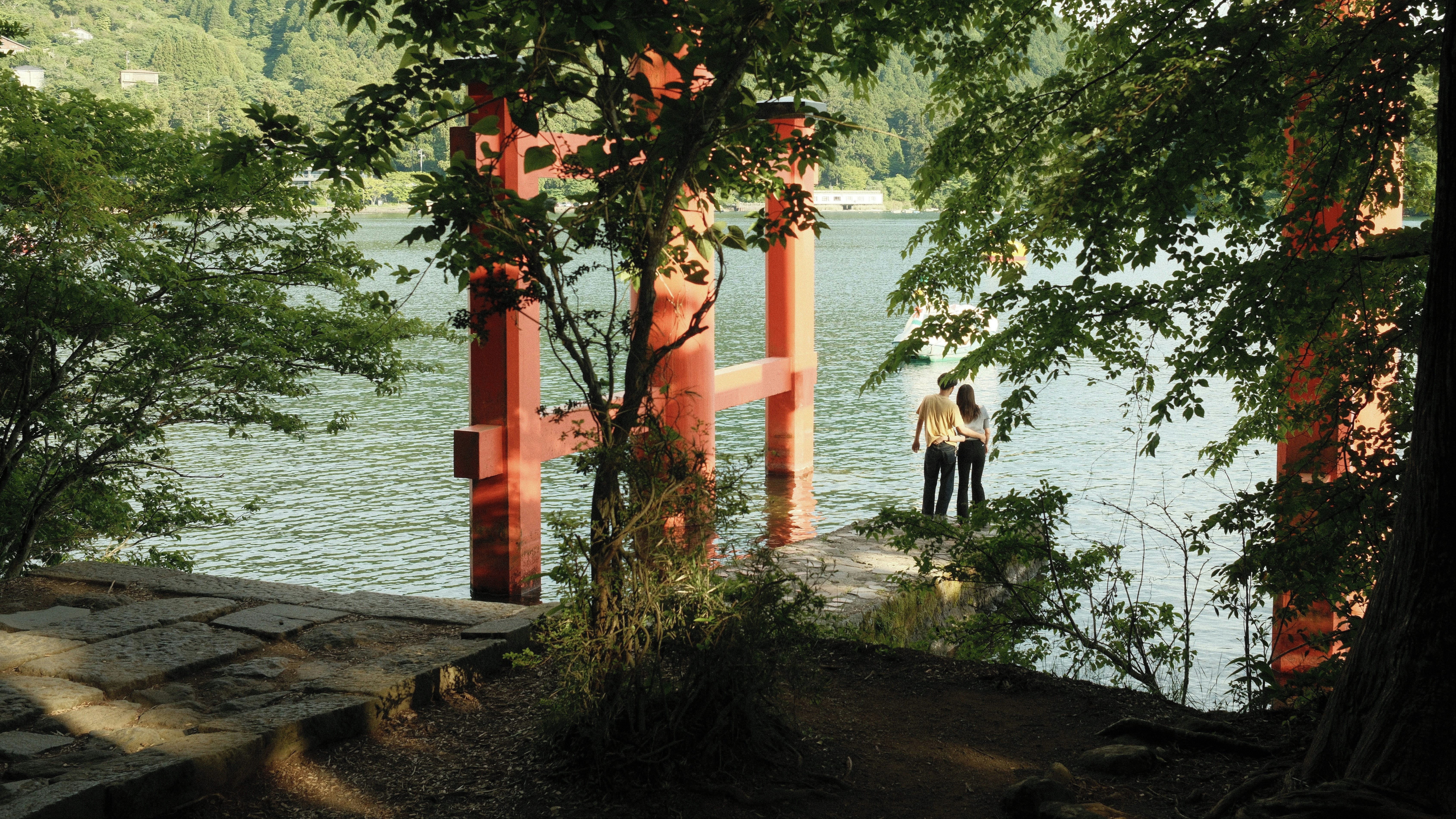 Red torii gate in a lake with people and trees.