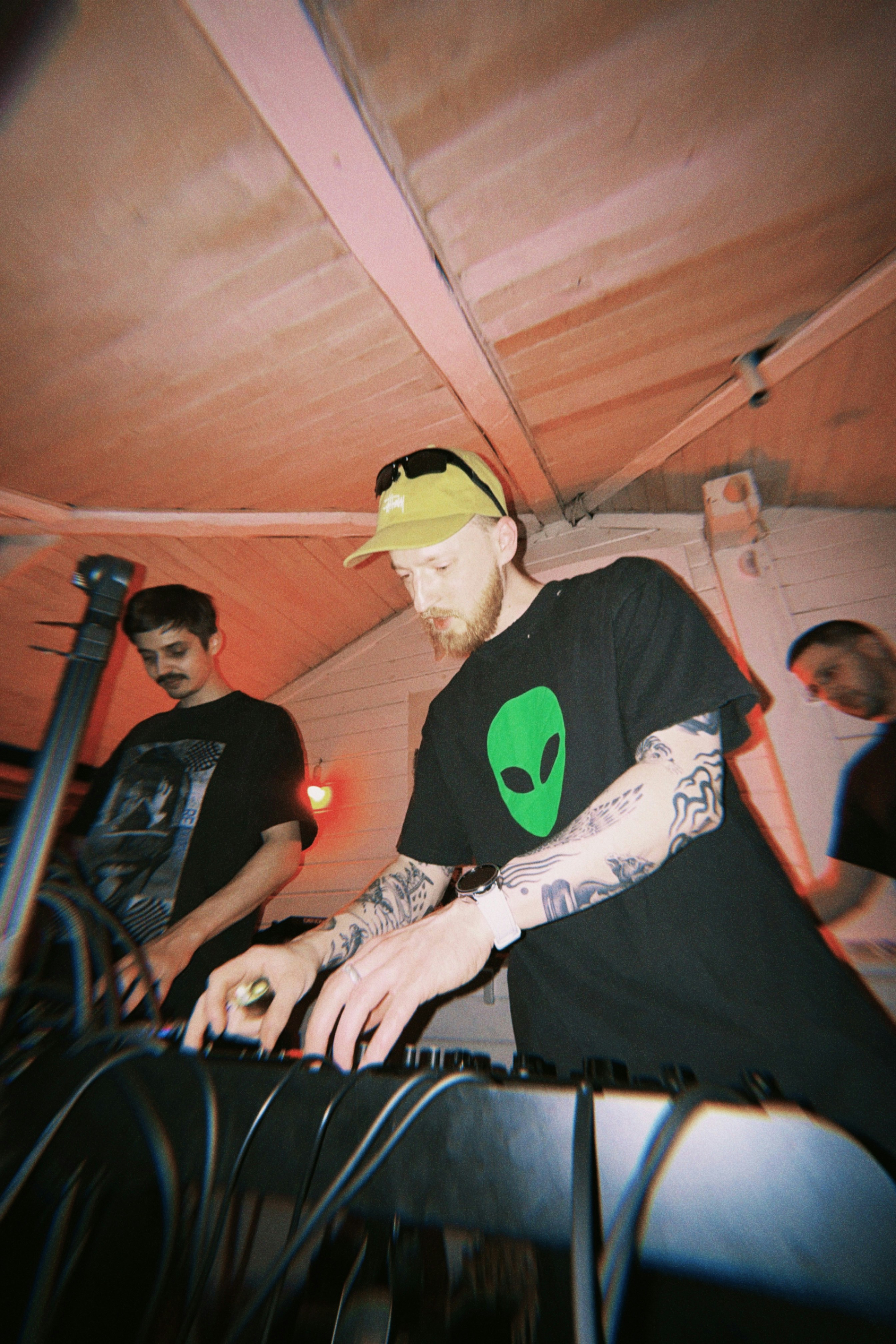 Man with alien shirt operates dj equipment at an event.