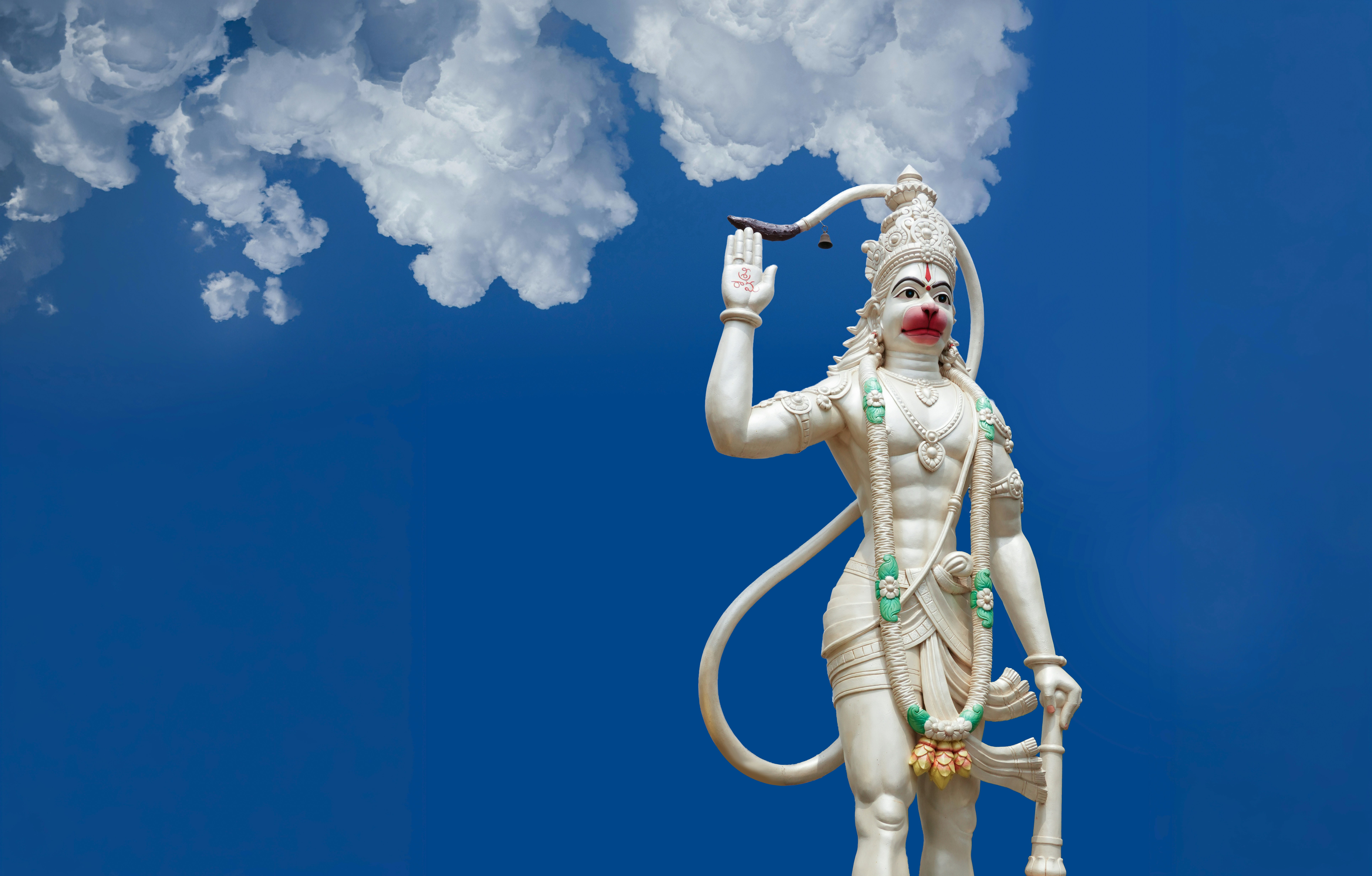 White hanuman statue stands against a clear blue sky.