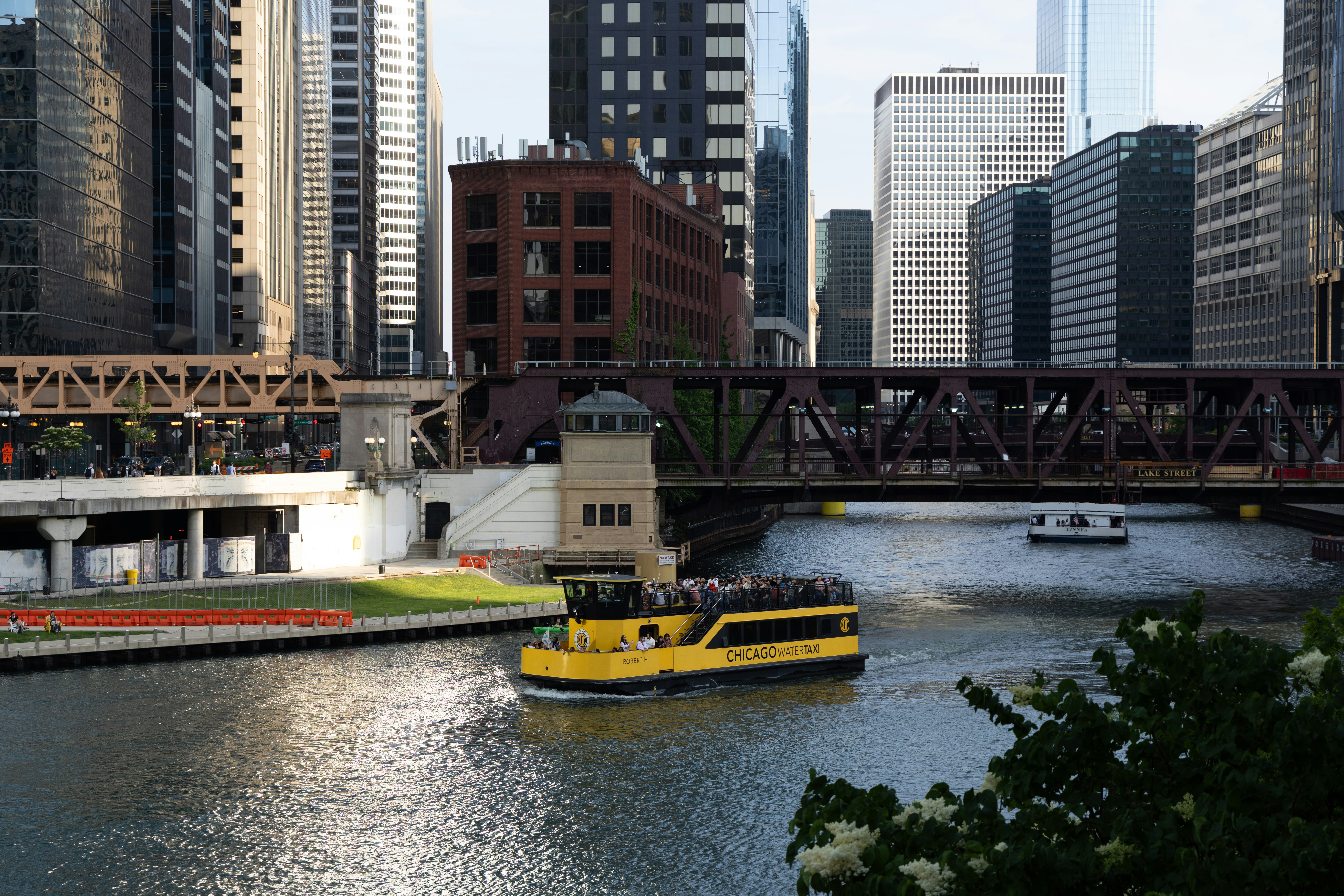 Yellow tour boat gliding under a steel bridge through a sunlit urban canal