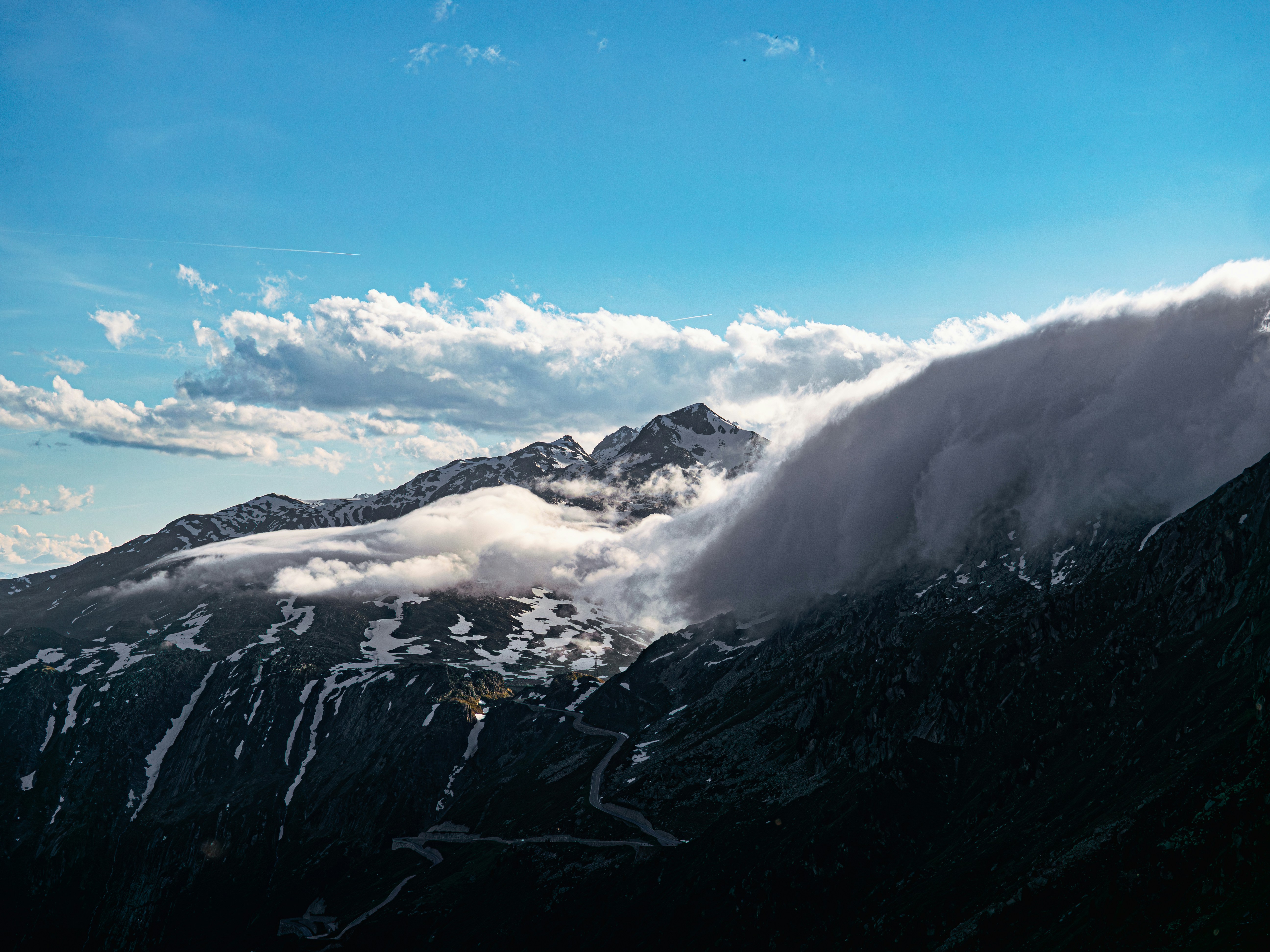 Misty Crest: A Winding Ribbon Clings to Alpine Slopes Under Clear Blue Sky