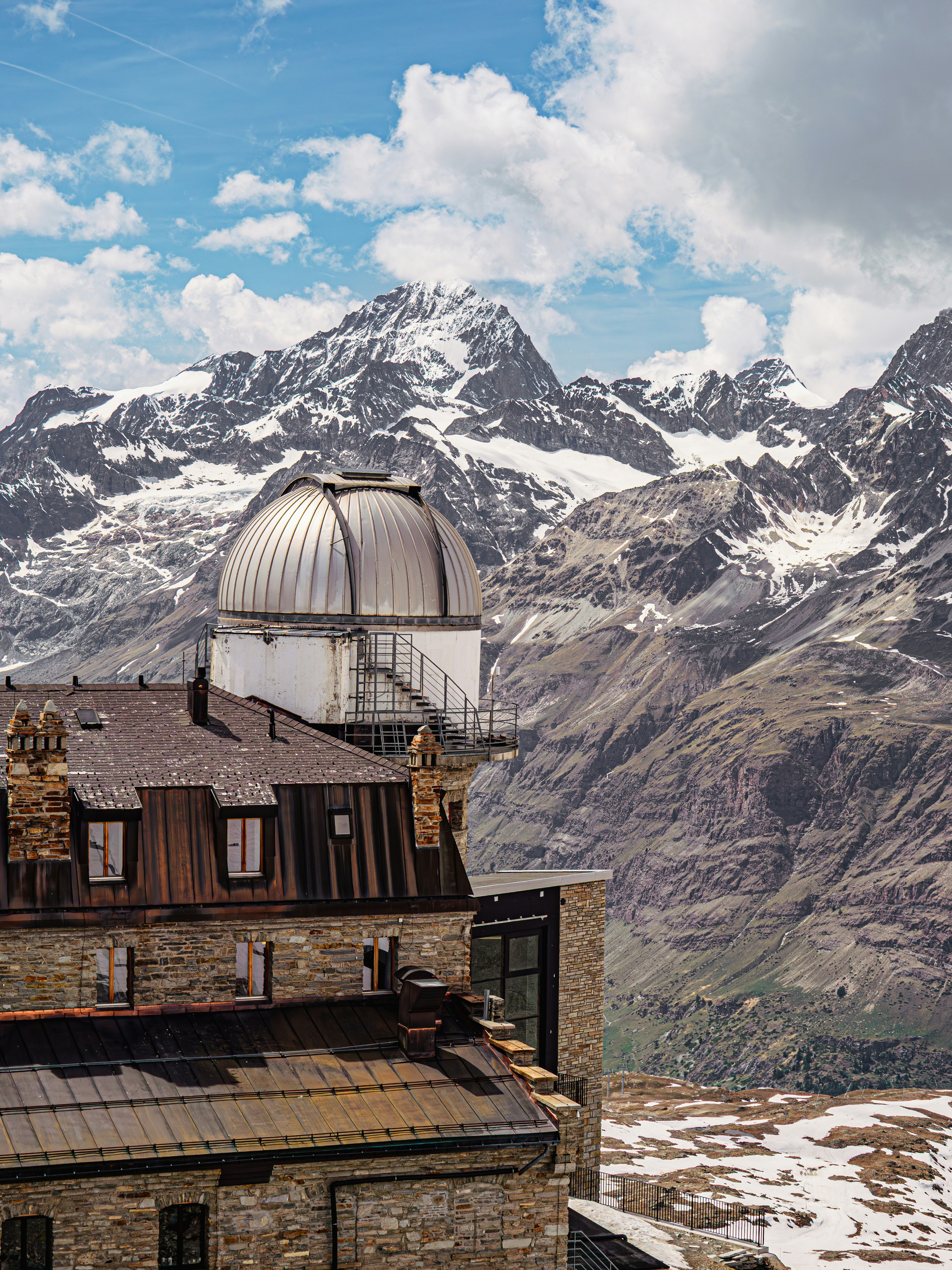 Observatory and stone building against majestic snow-capped mountains.