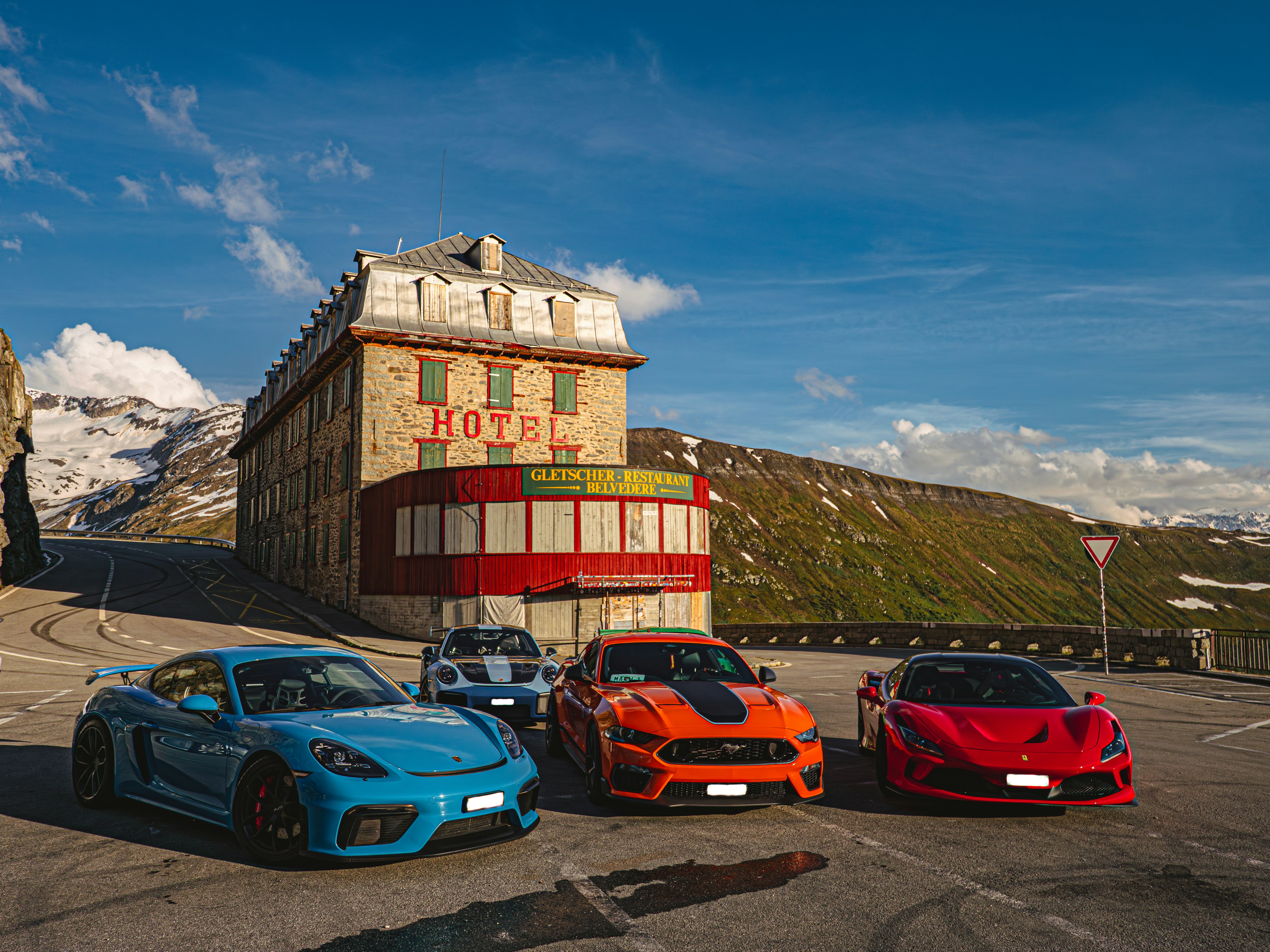 Four sports cars parked in front of a mountain hotel.