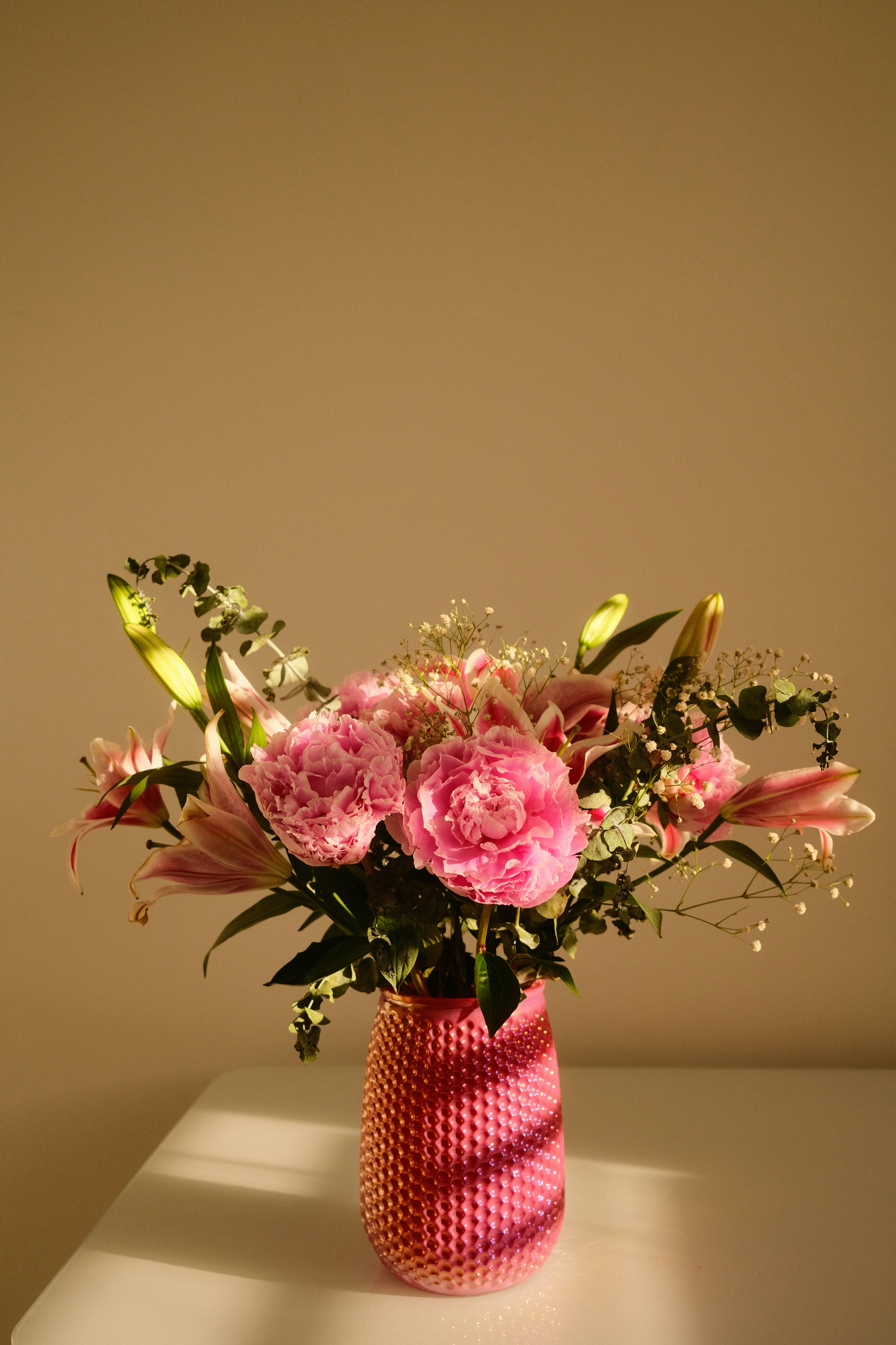 Pink Peony Bouquet in a Textured Vase Beneath Warm Light