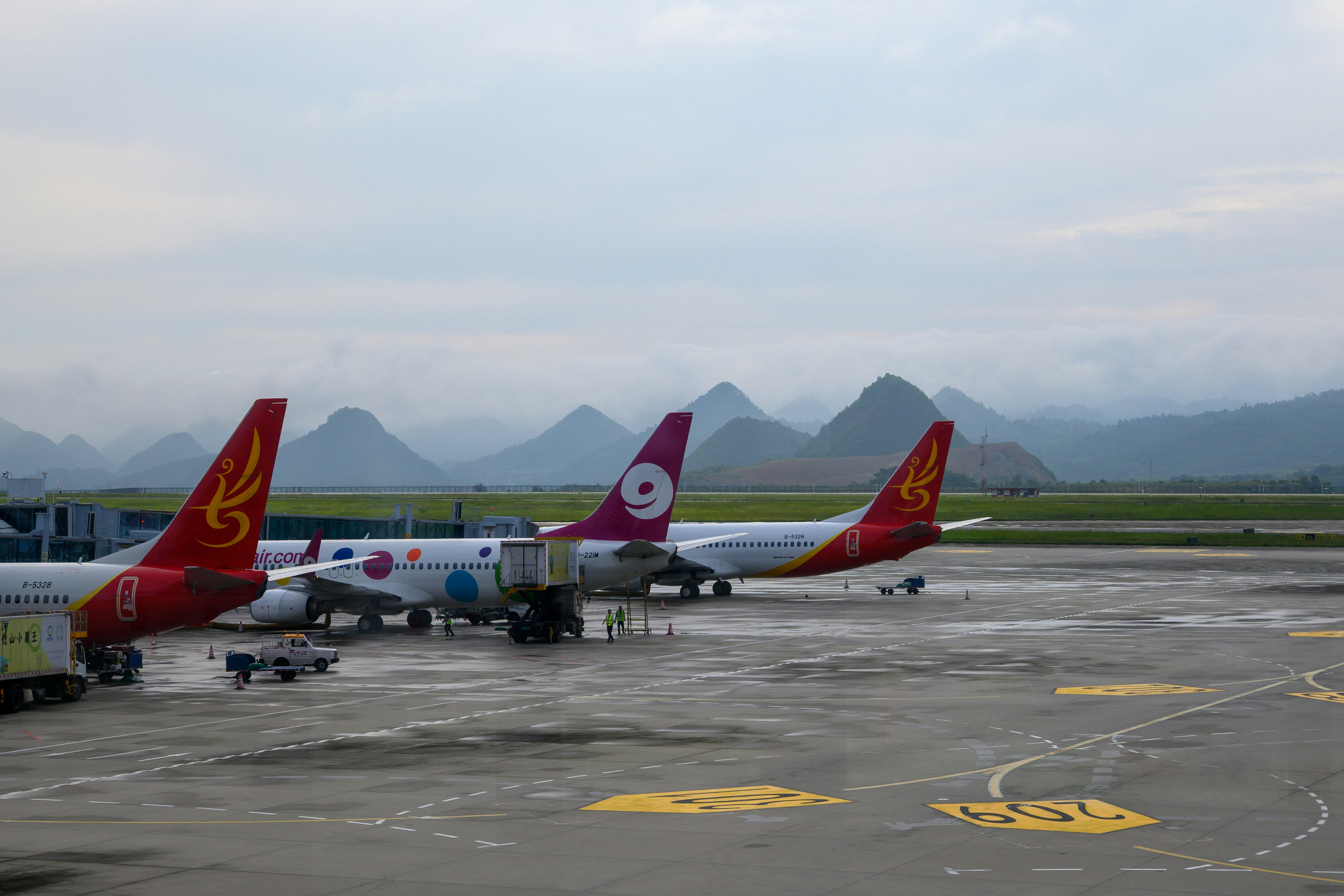 Row of colorful jetliners at a quiet tarmac under distant karst hills