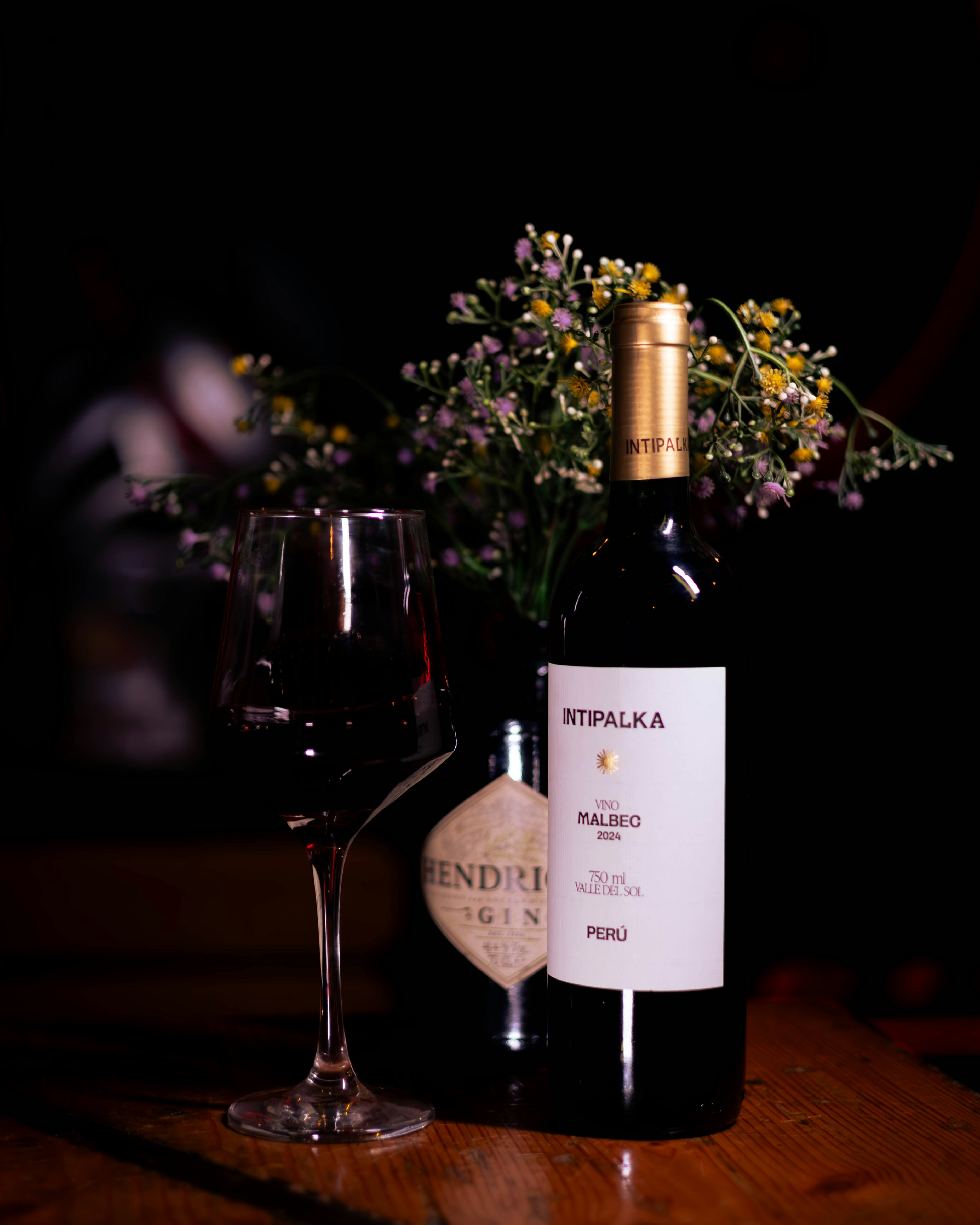 Wine glass, bottle, and floral bouquet on a dimly lit table