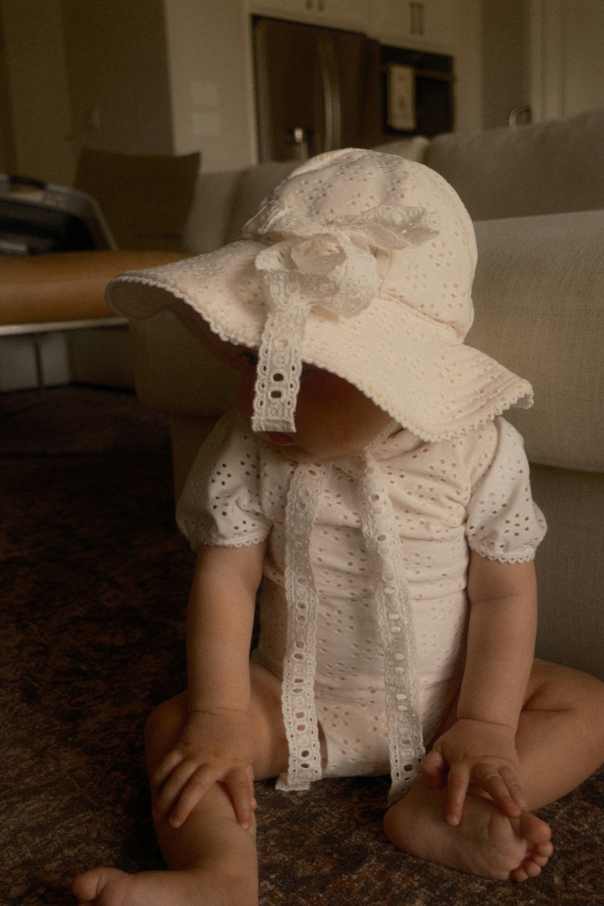 Innocent Quiet: A Baby Doll in a Lace Sunhat on a Living Room Floor