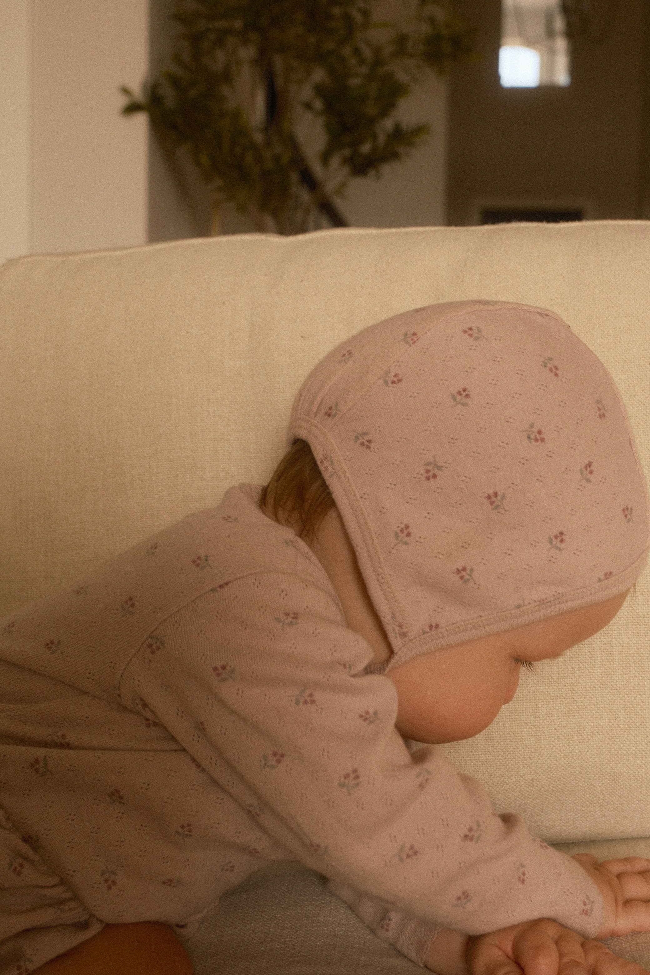 Soft-caped infant at rest on a pale sofa with a floral hood