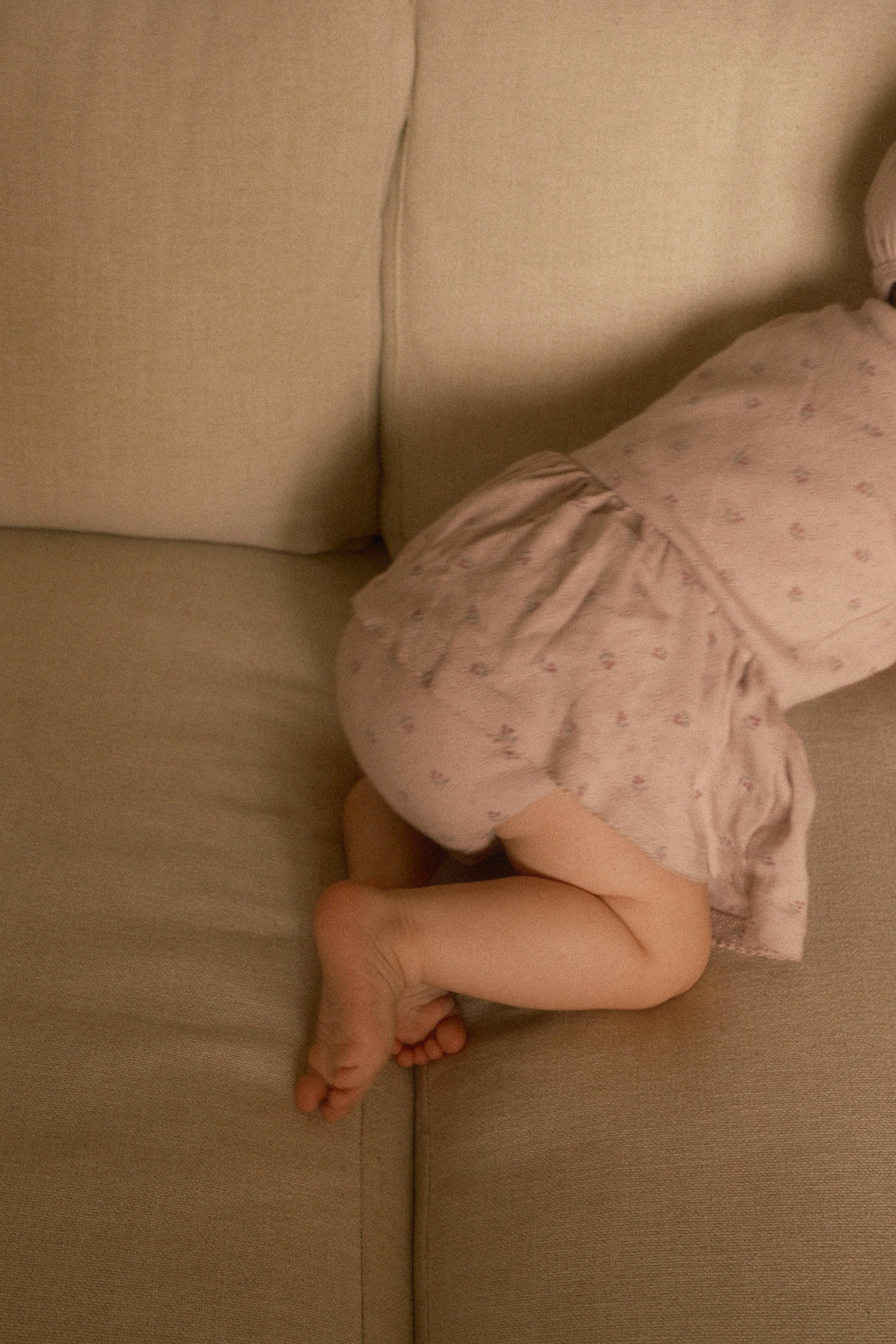 A baby sleeping on a beige couch.