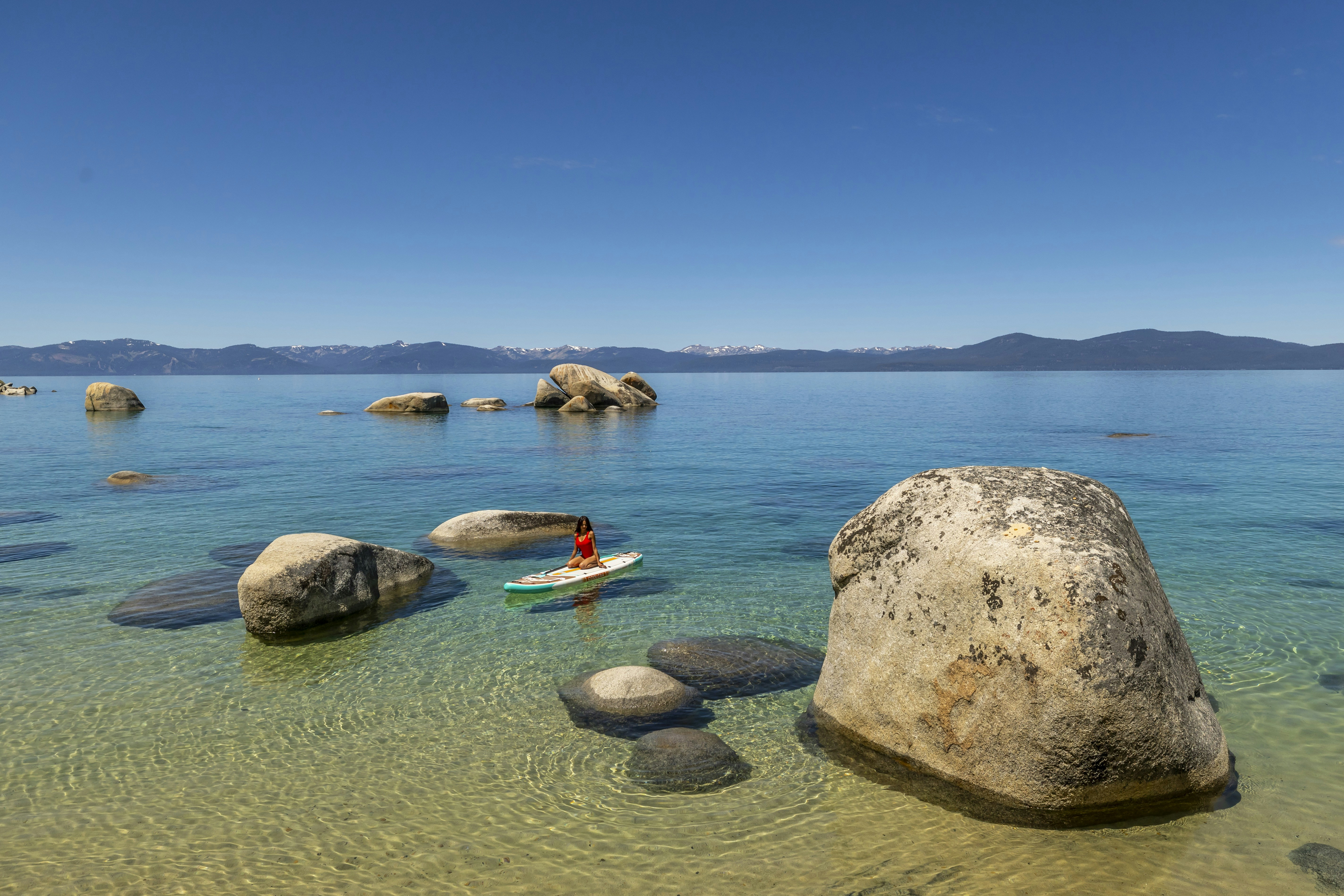 Solitary kayaker among sunlit boulders in turquoise shallow waters