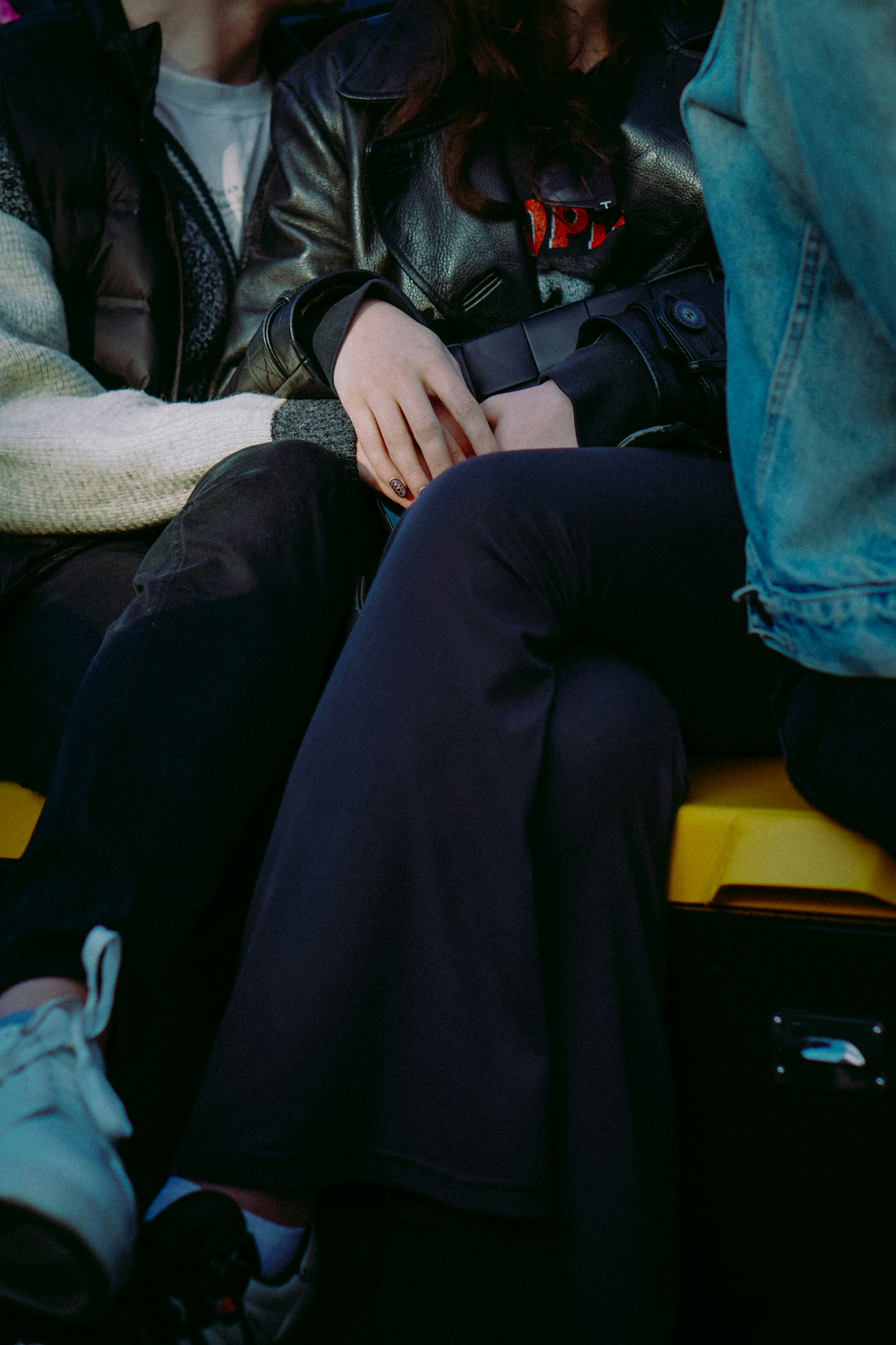 Seated trio: hands resting over laps on a sunlit yellow bench