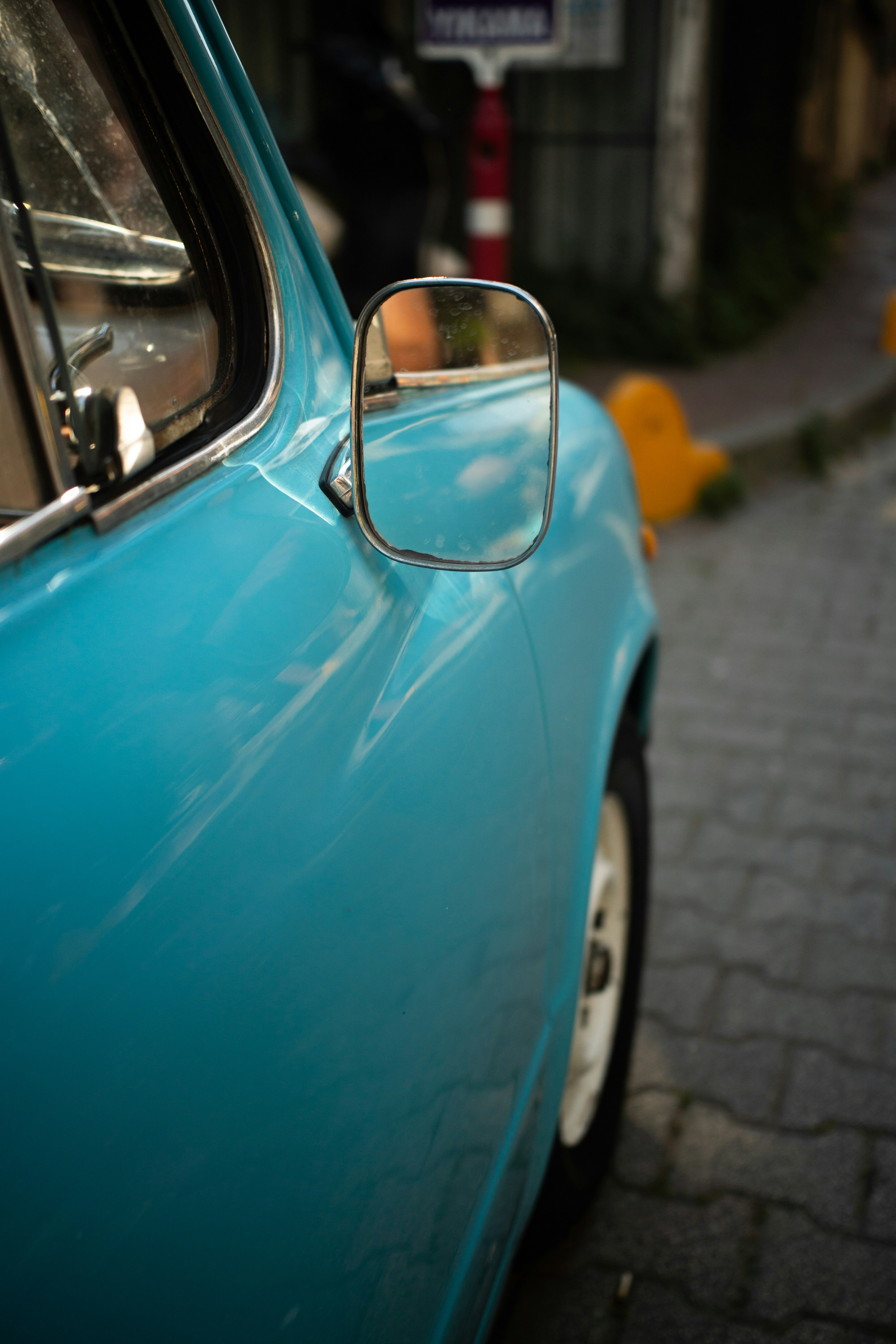 A vintage turquoise car parked on a cobblestone street.