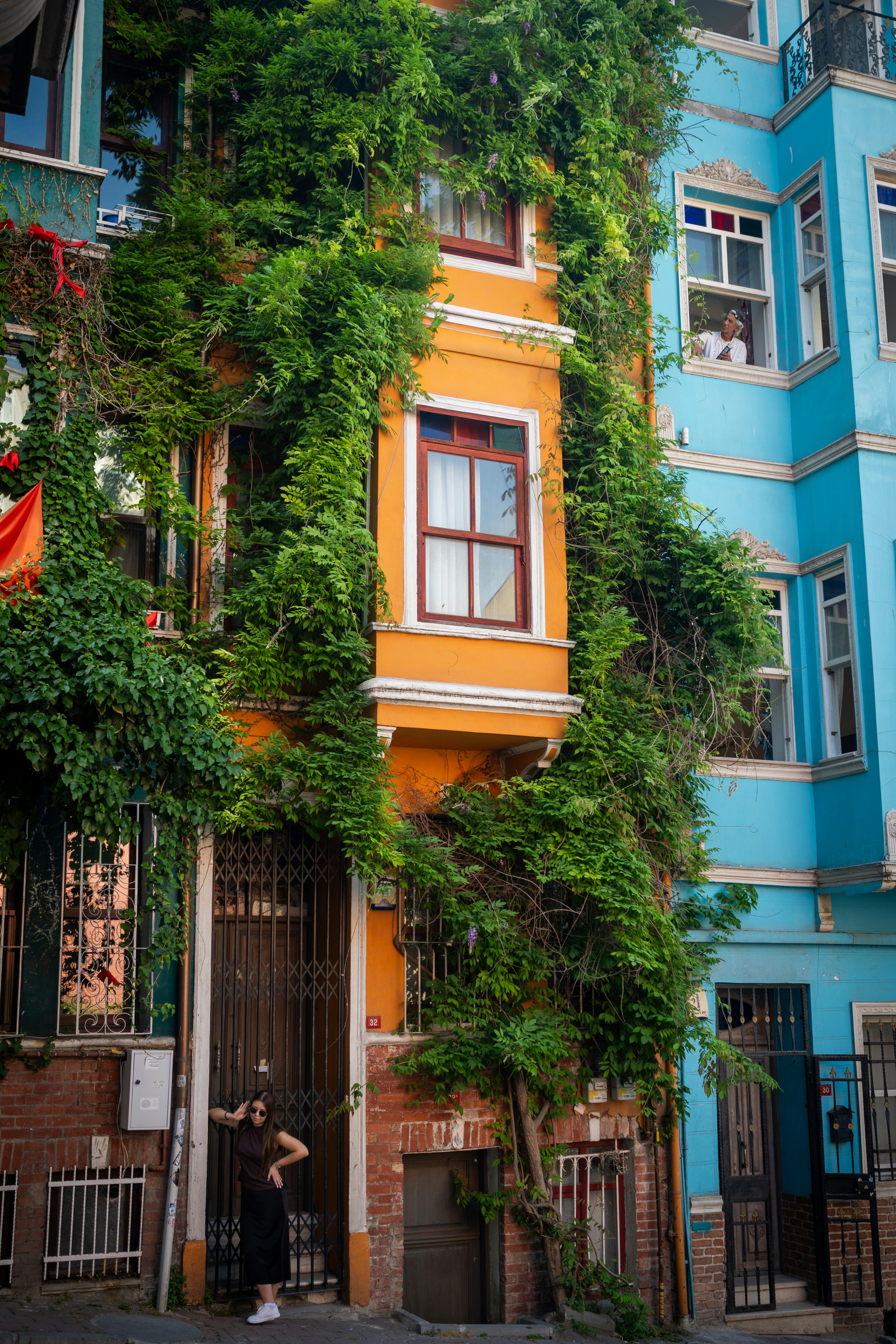 Woman by vibrant orange building covered in green foliage.