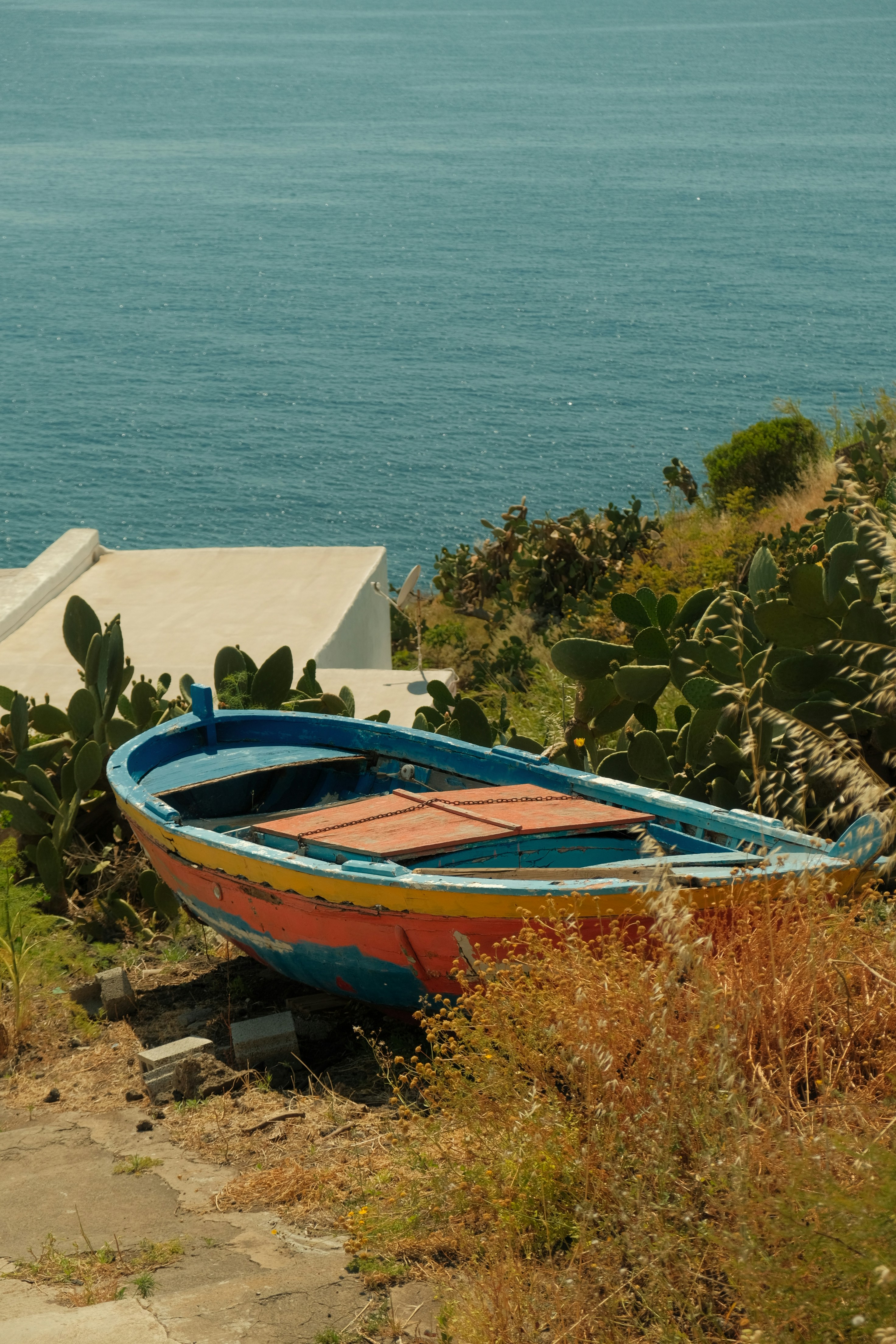 Weathered boat by a terraced coastline with cactus and sea beyond