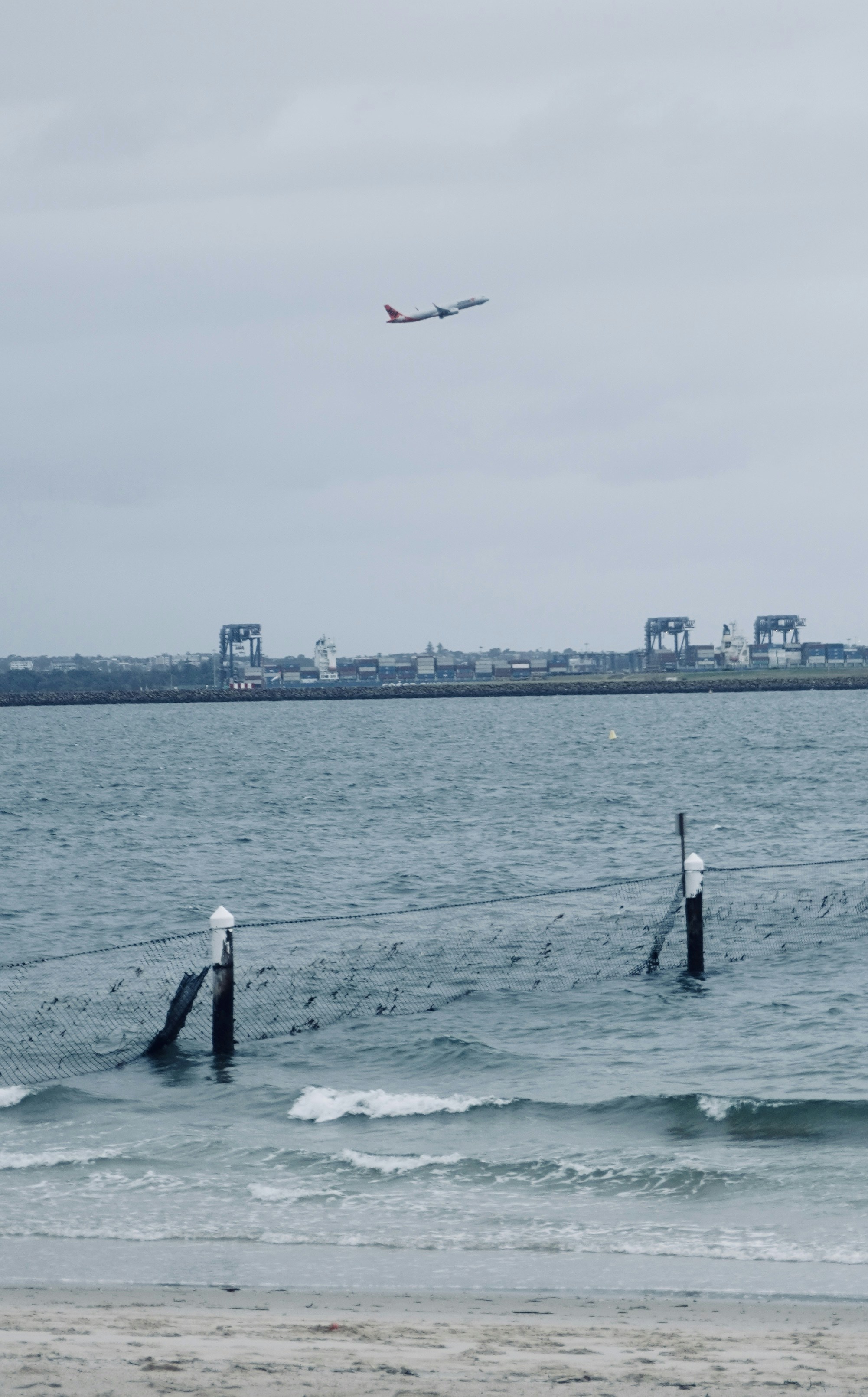 Coastal Quiet: A Plane Traces the Horizon Beyond Industrial Silhouettes