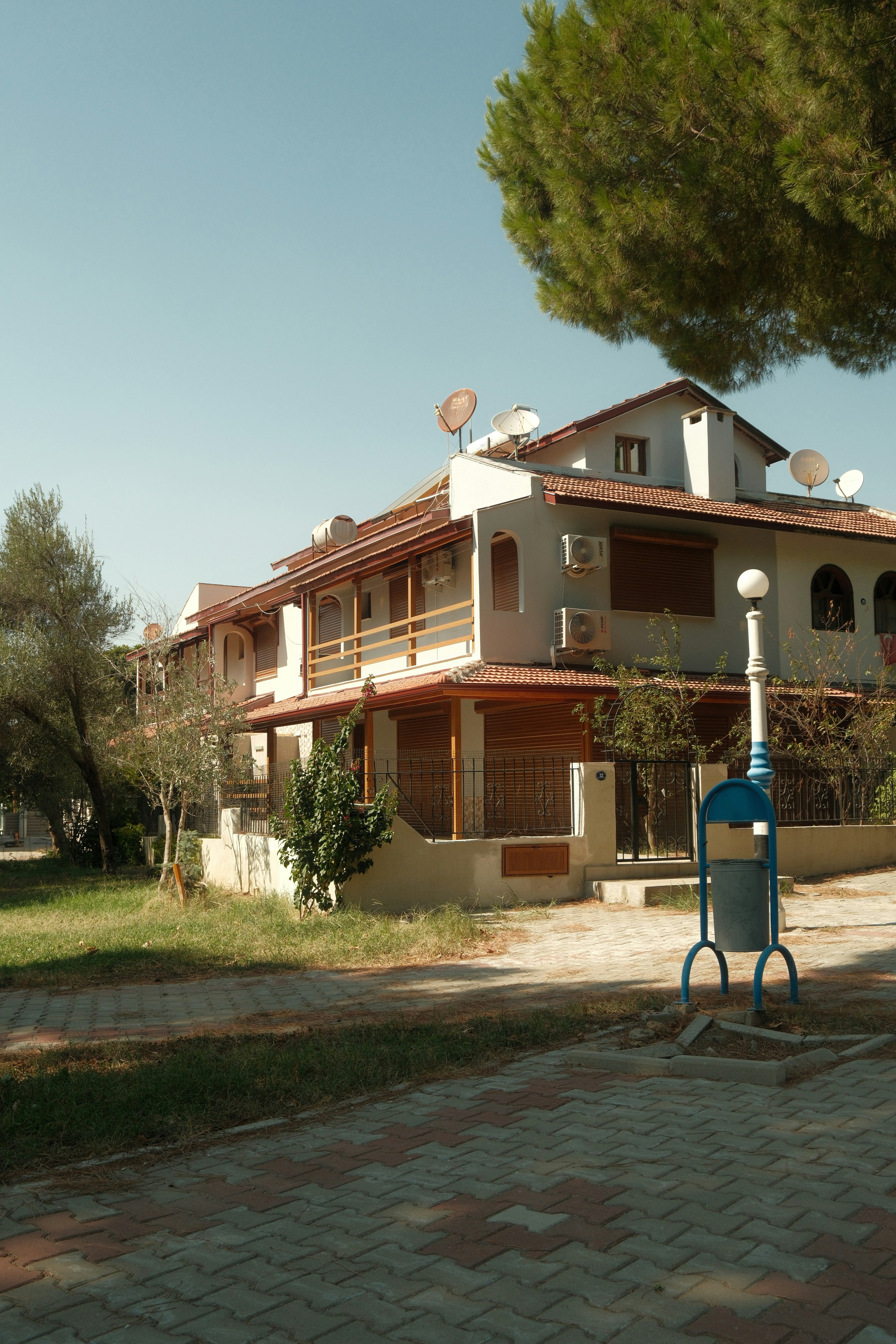 Sunlit Mediterranean Suburb: A Two-Story Home Framed by Pine and Shadow