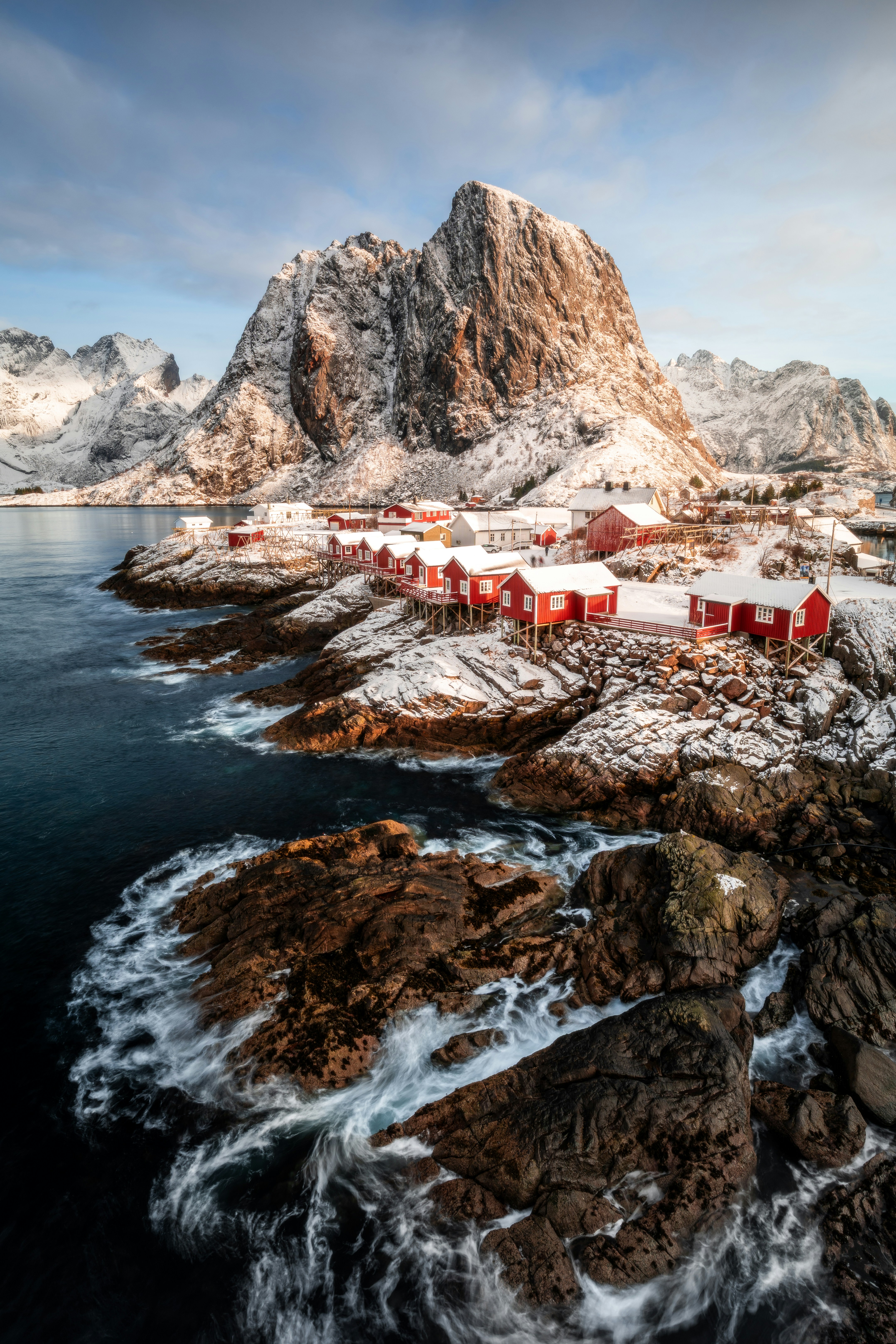 Snowy village with red houses, rocky coast, and majestic mountains.