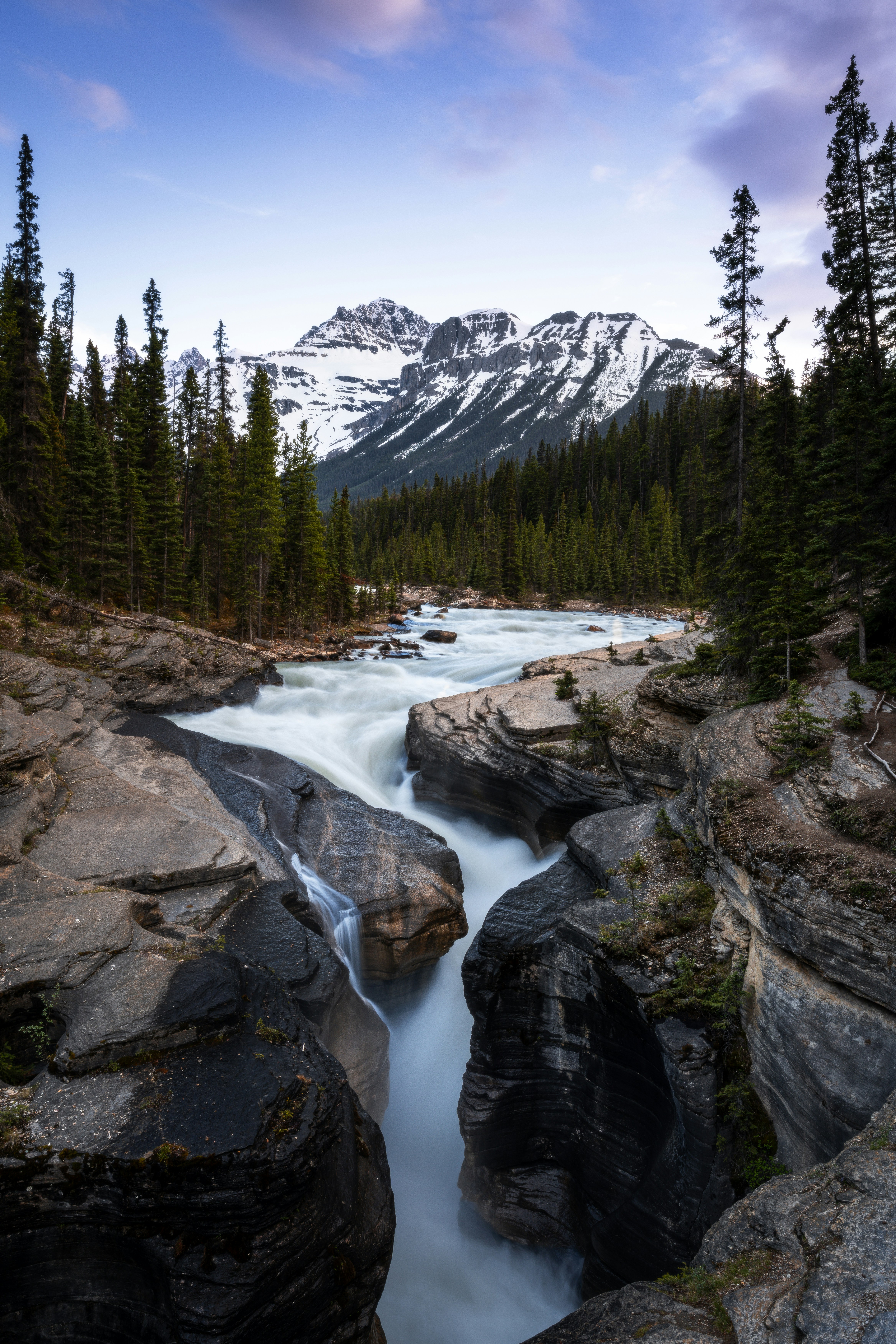 Silky river flows through a rocky canyon with snowy mountains.