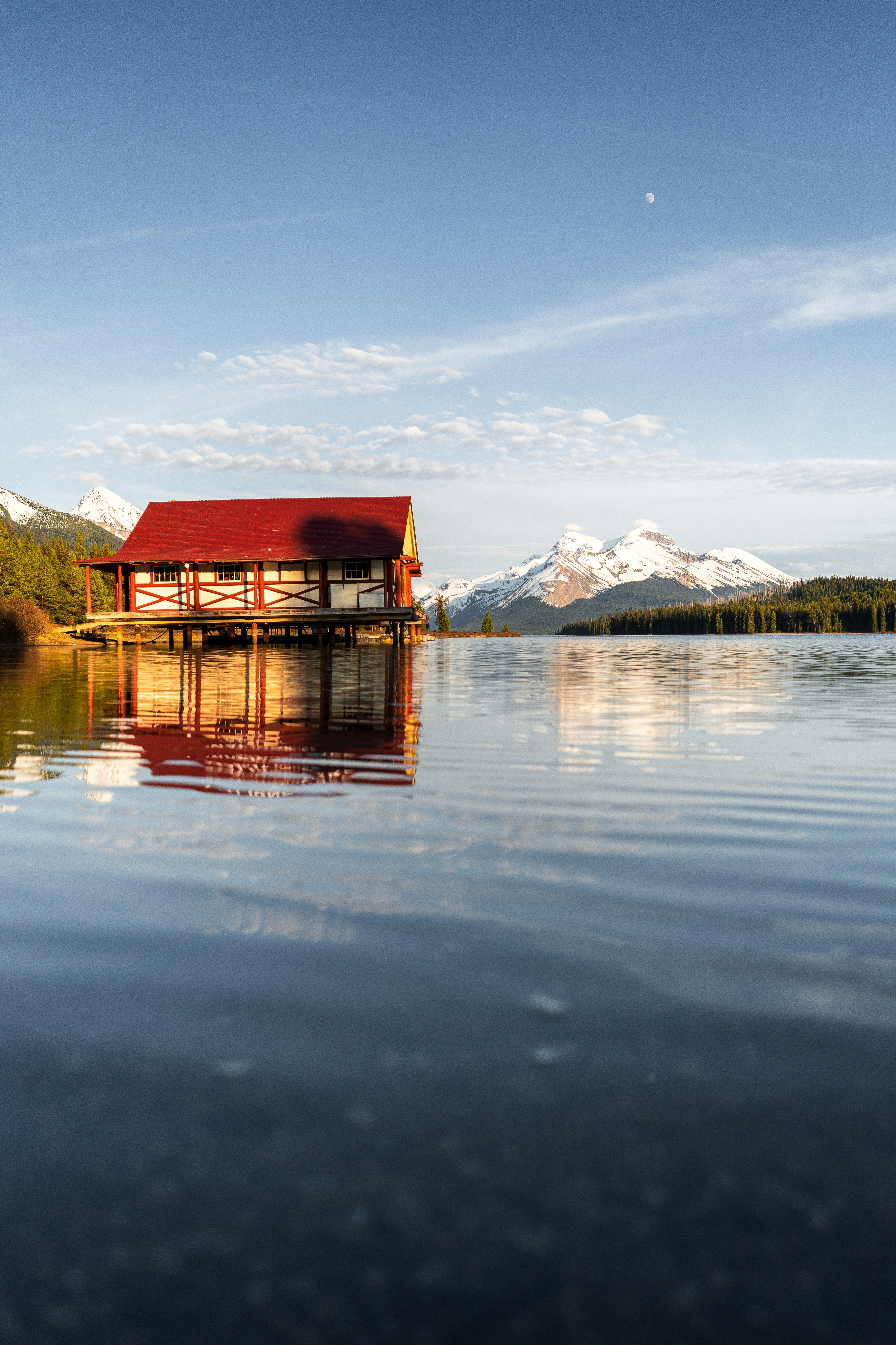 Red-roofed boathouse on a glassy alpine lake at sunrise
