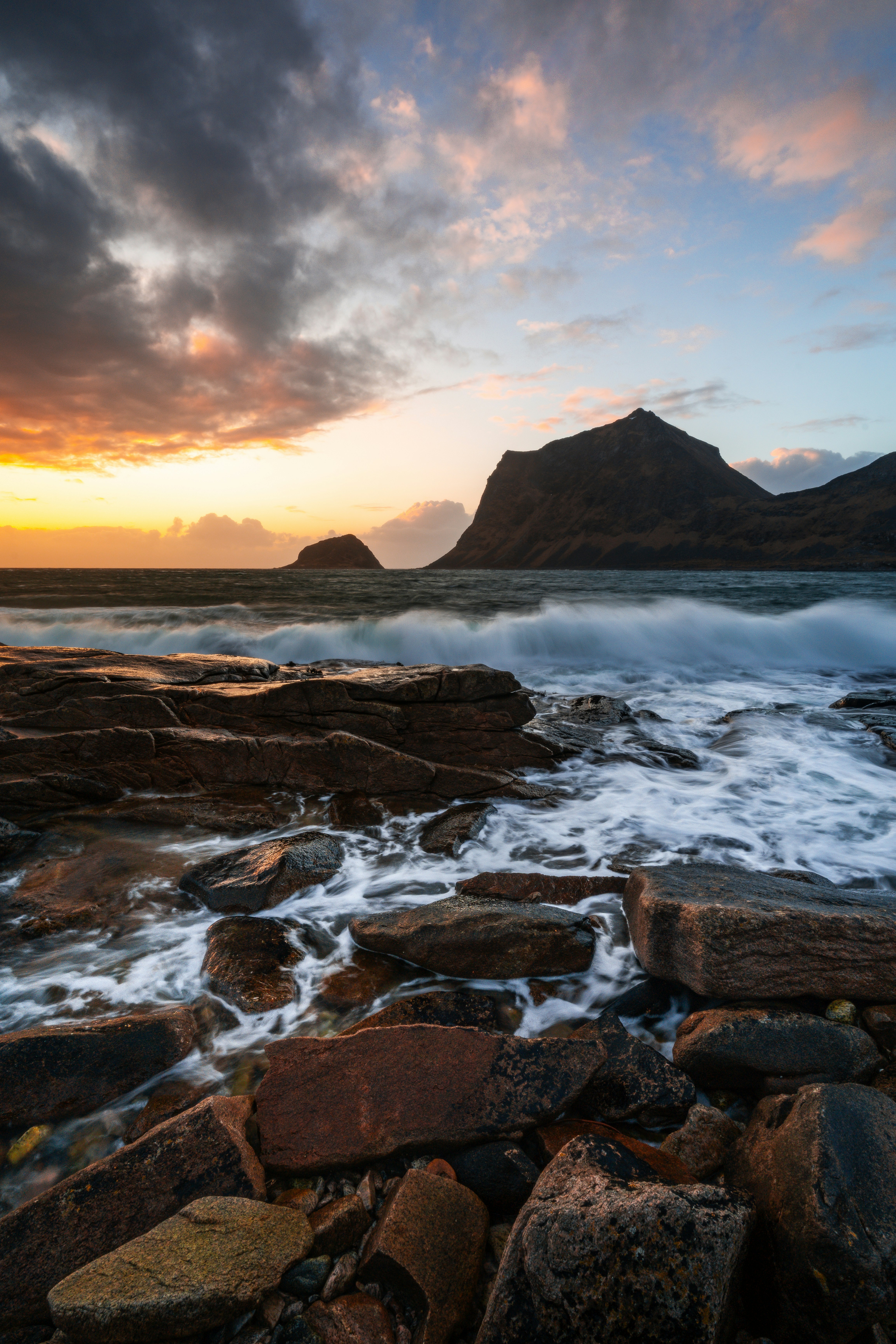 Sunset on jagged shores: waves, rock silhouettes and a distant island