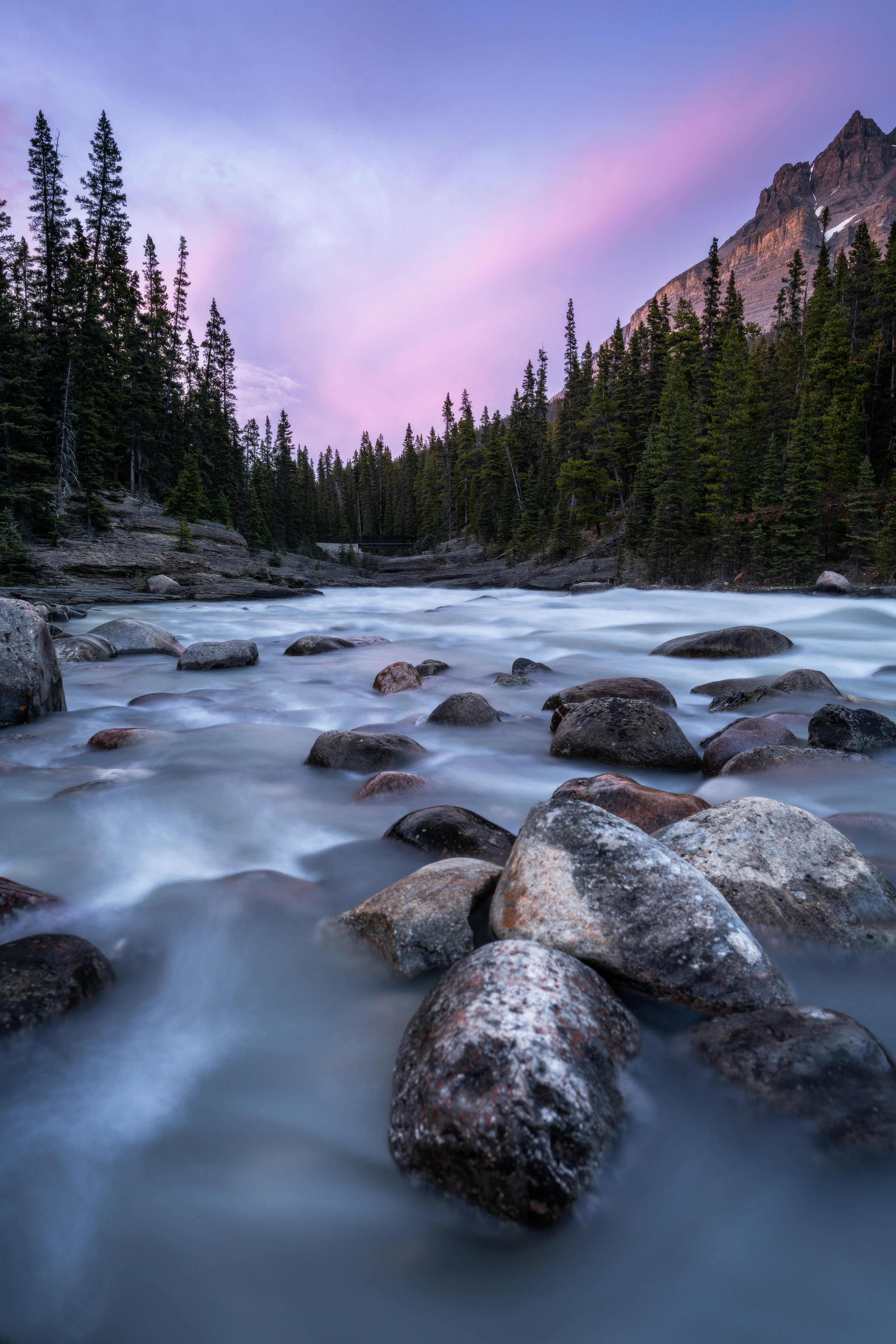 Misty Torrent at Twilight: Stones, Forest, and Pink-tinged Clouds