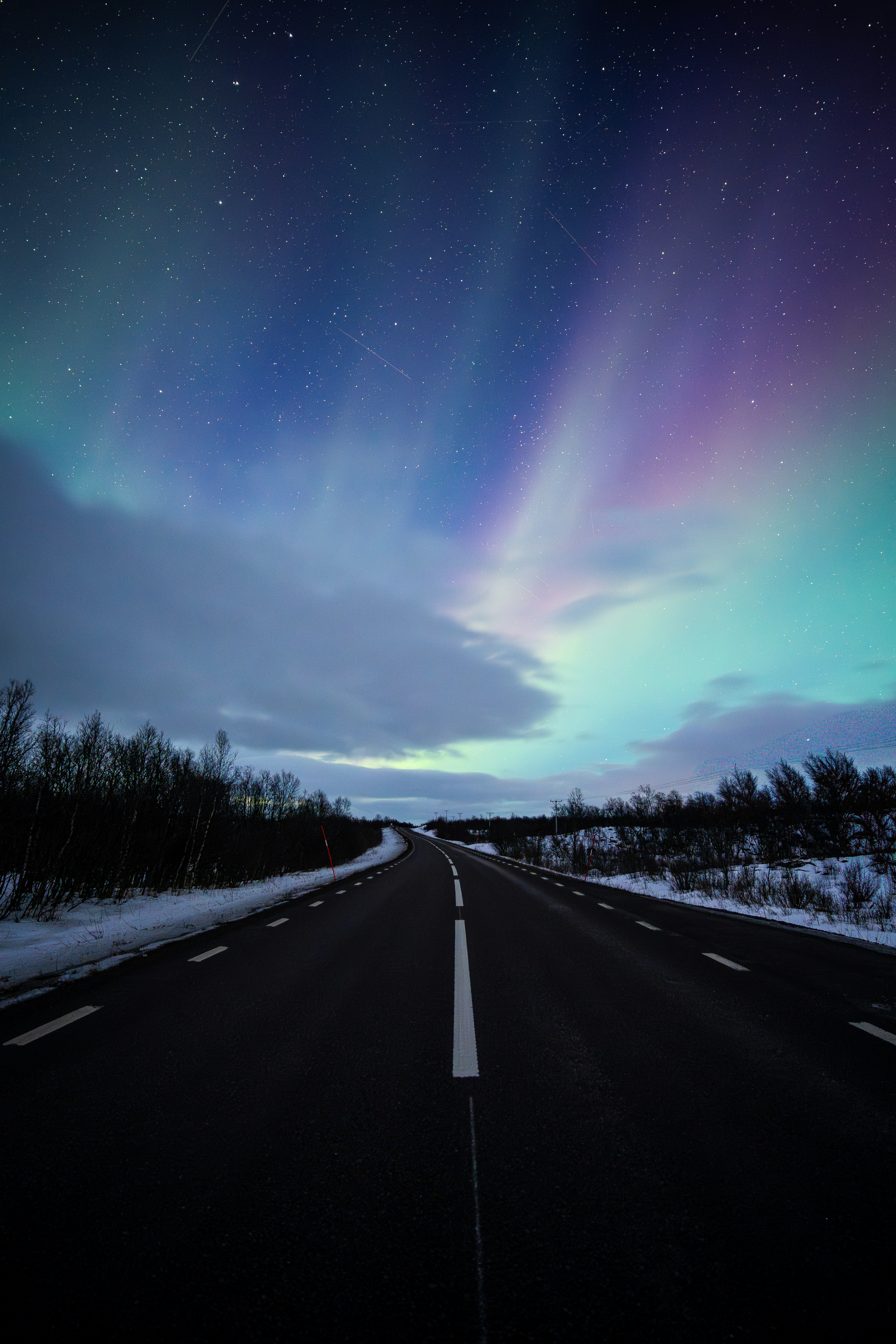 Aurora borealis over a snowy road and starry night.