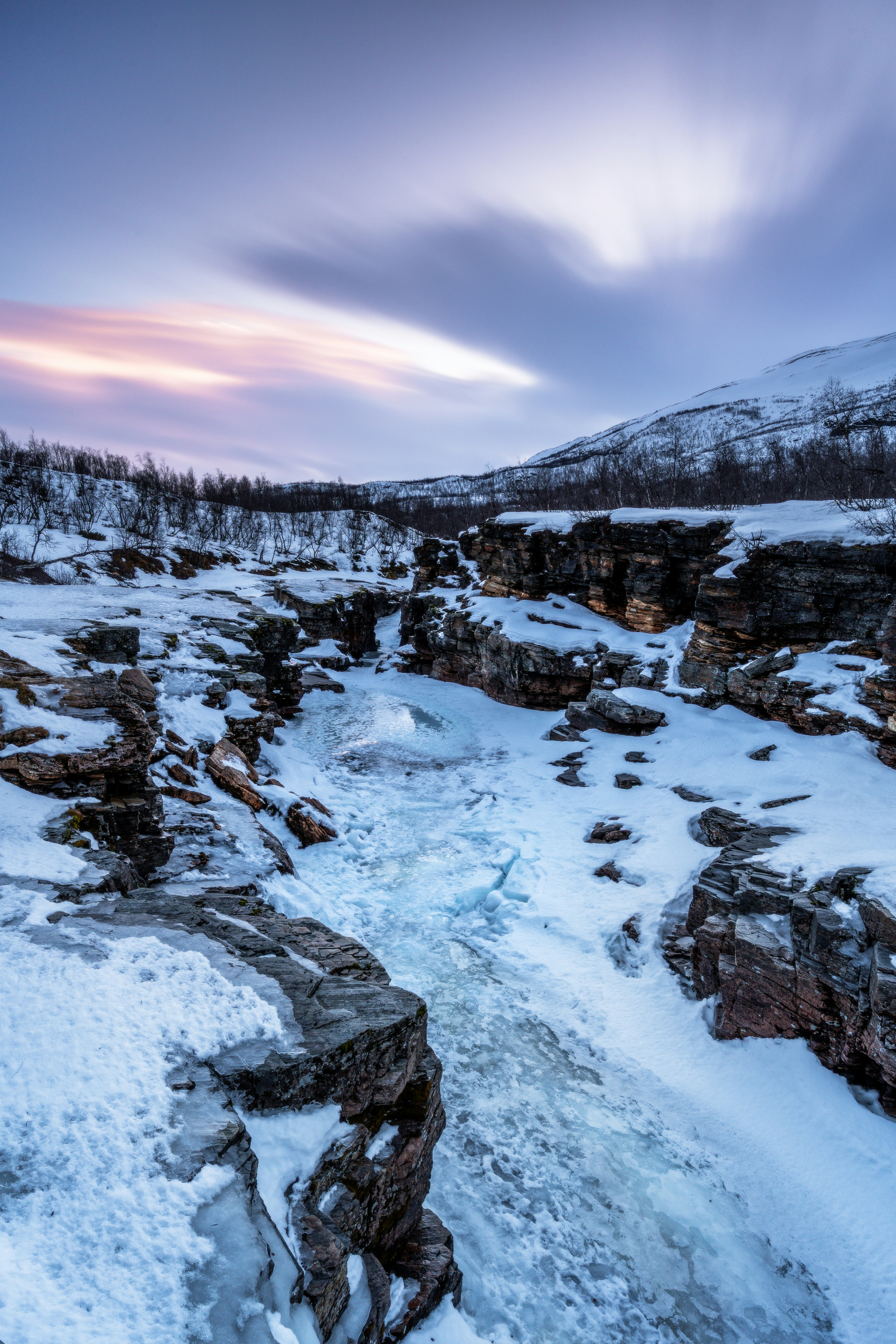 Icy river winding through a snow-covered canyon at dusk.