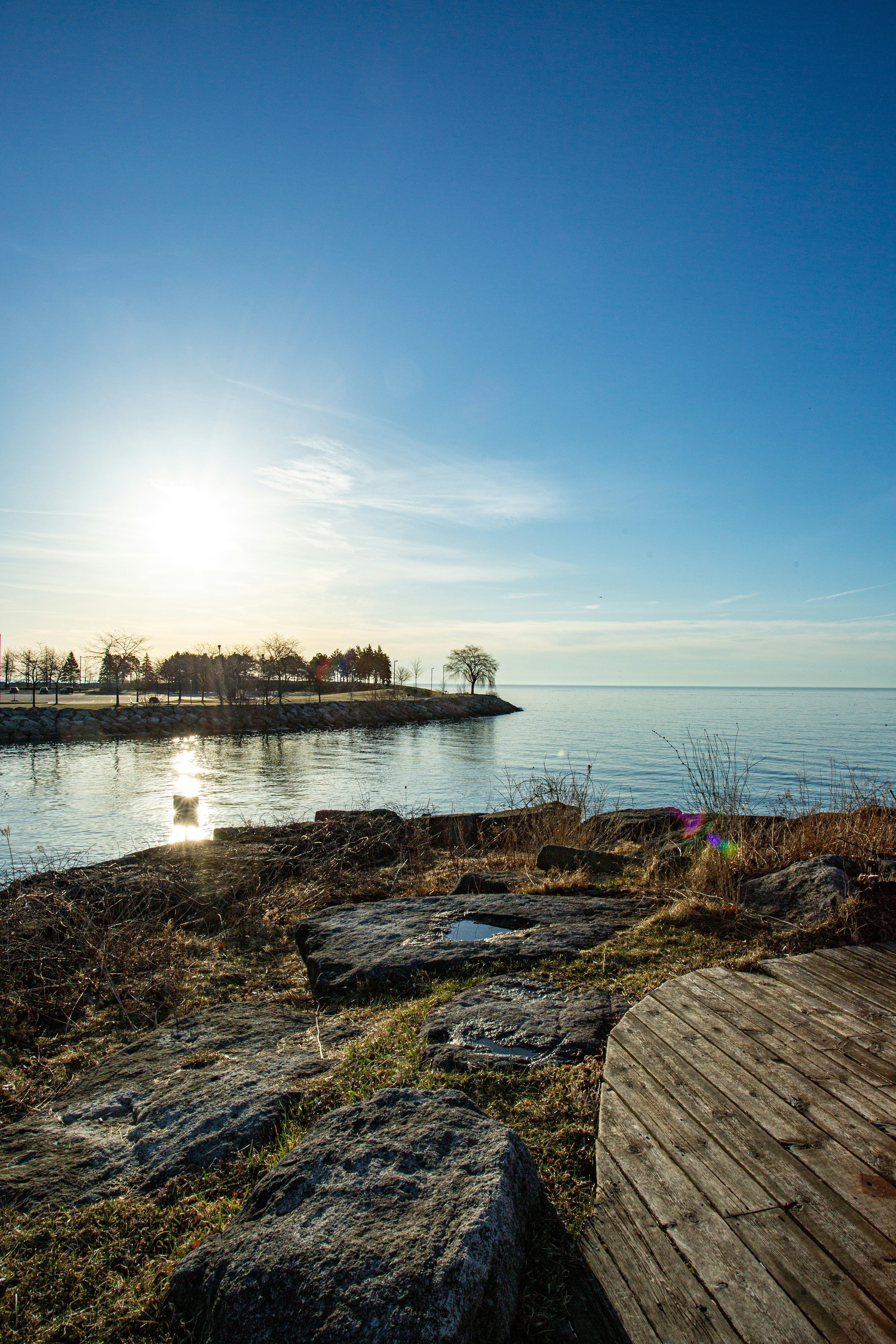 Sunlit shoreline with a lone jetty and rocky foreground