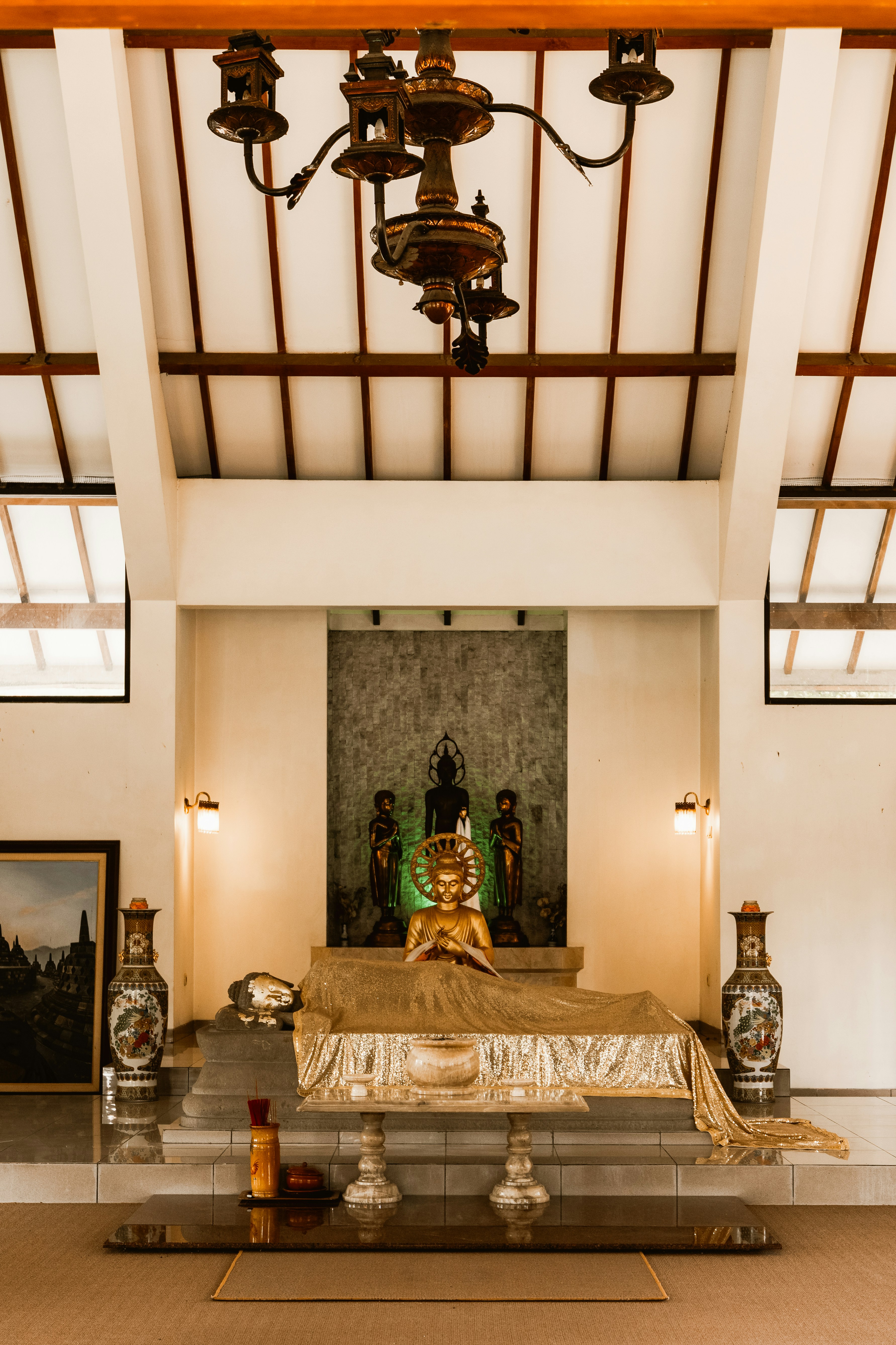 Quiet Reverence under a Looming Chandelier: Buddhist Altar Inside a Sunset-Hued Hall