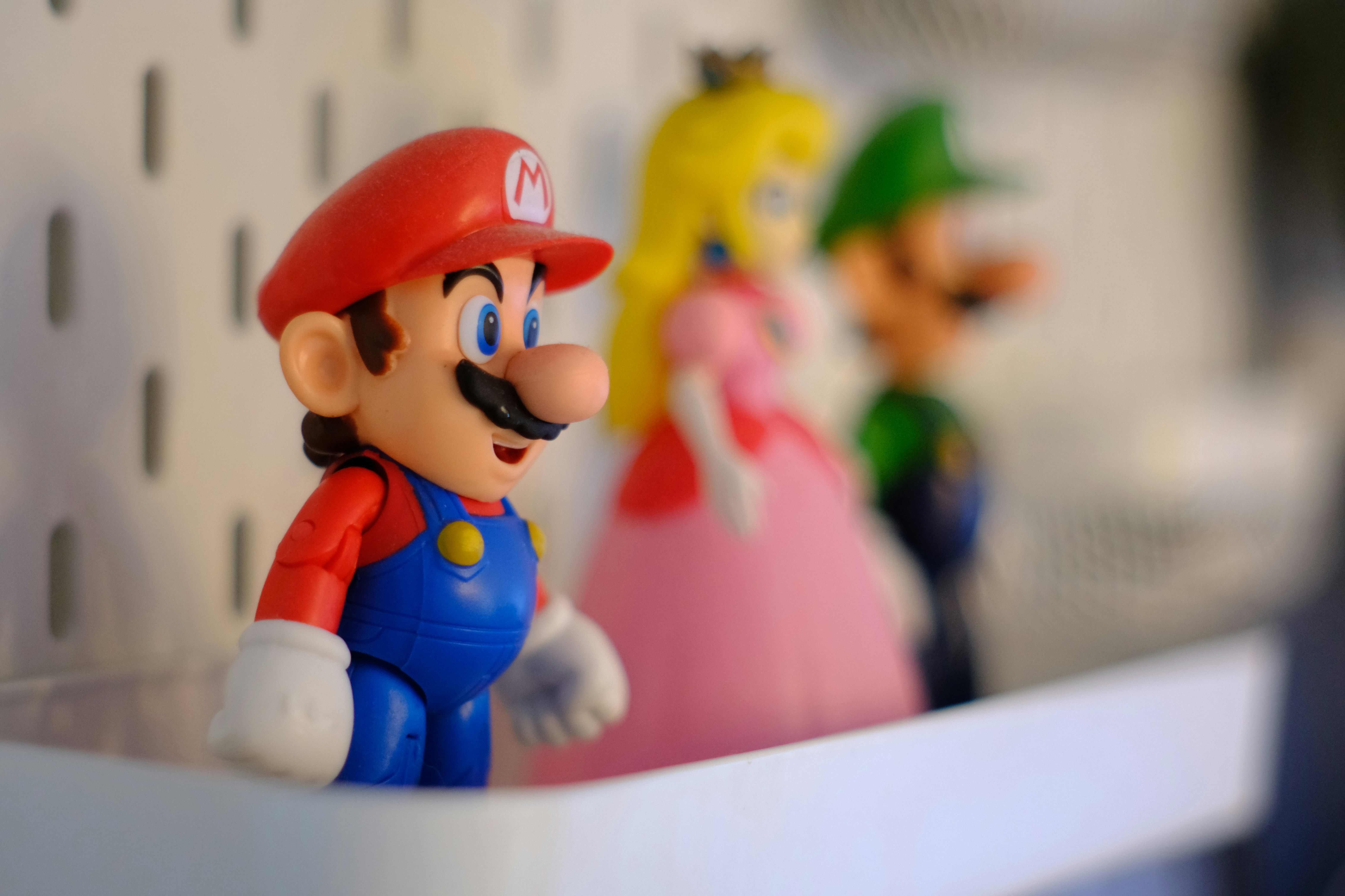 Mario, princess peach, and luigi figures on a white shelf.
