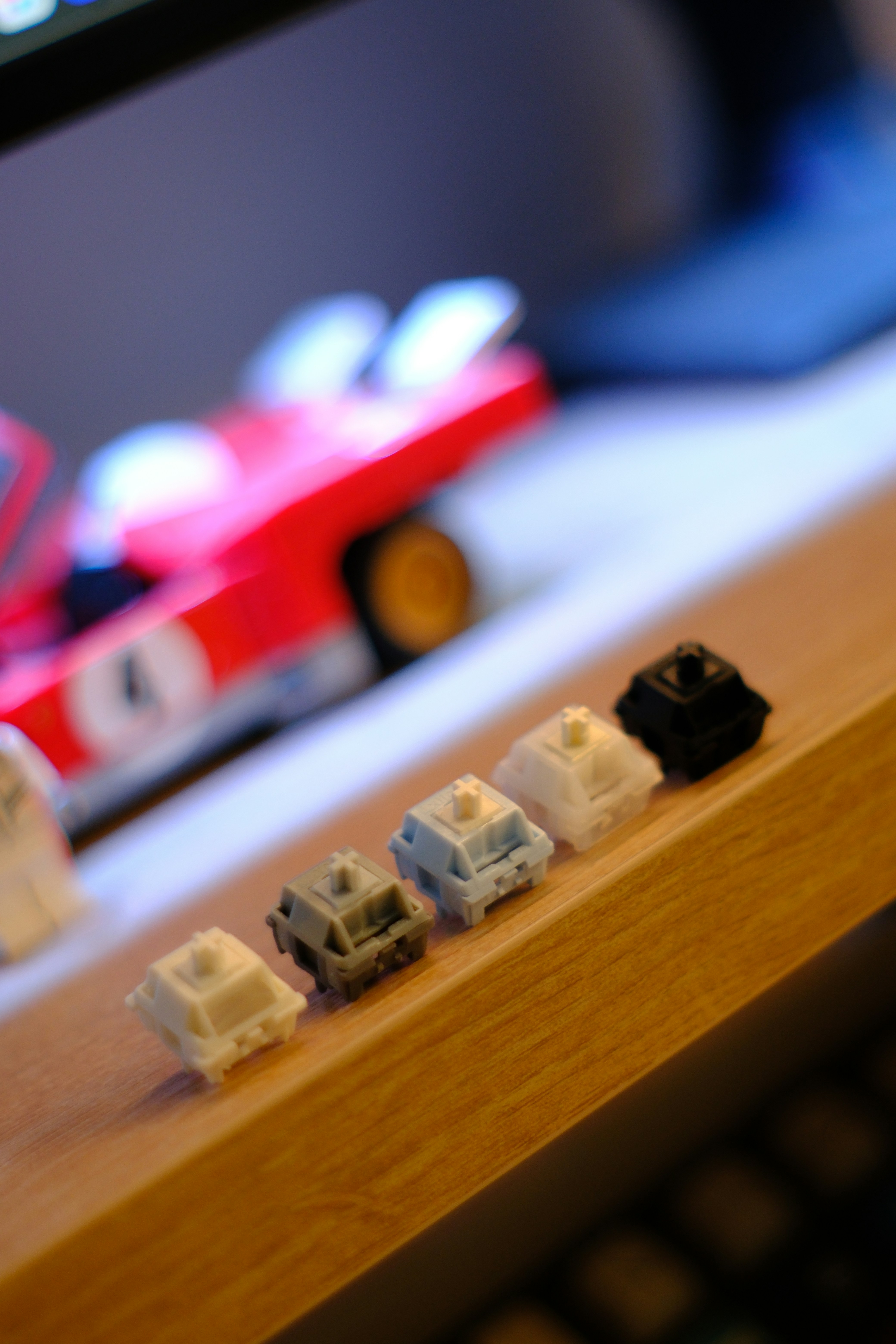 Row of Tiny Keyboard Switches on a Wood Rail with a Blurred Toy Car in the Background