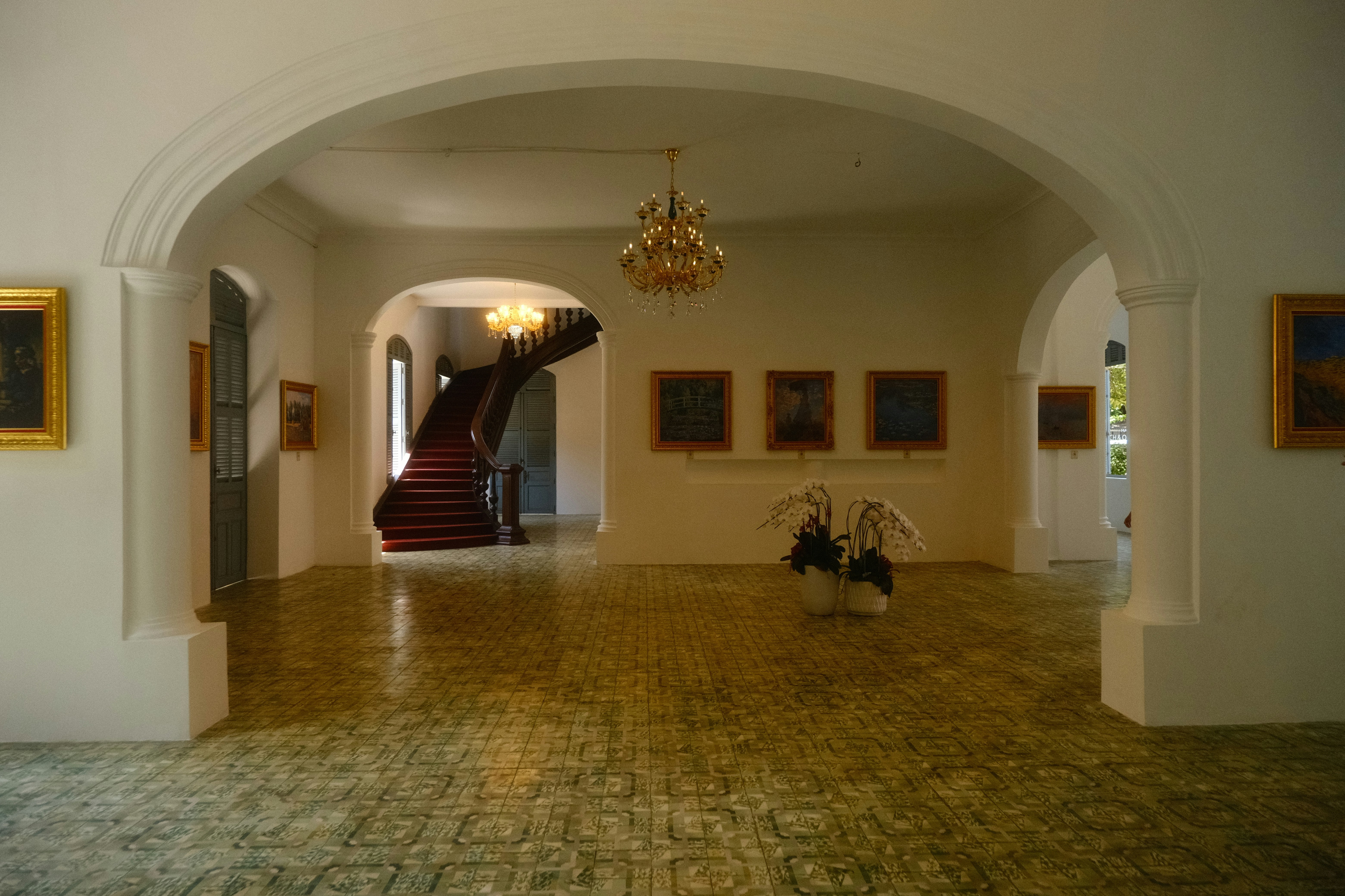 Elegant hall with a grand staircase, paintings, and chandelier.