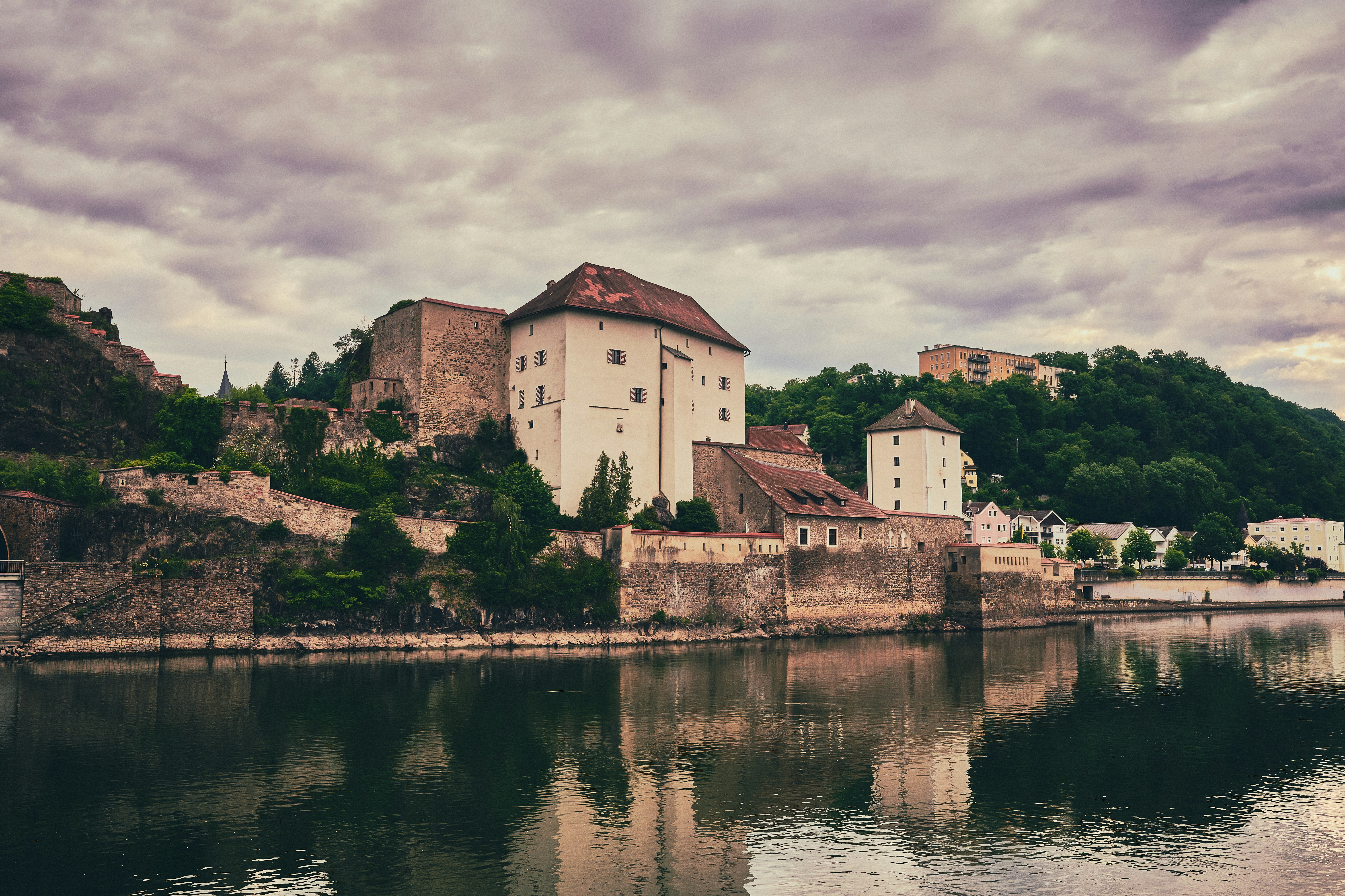 Riverside castle with reflections beneath a dramatic cloudy sky.