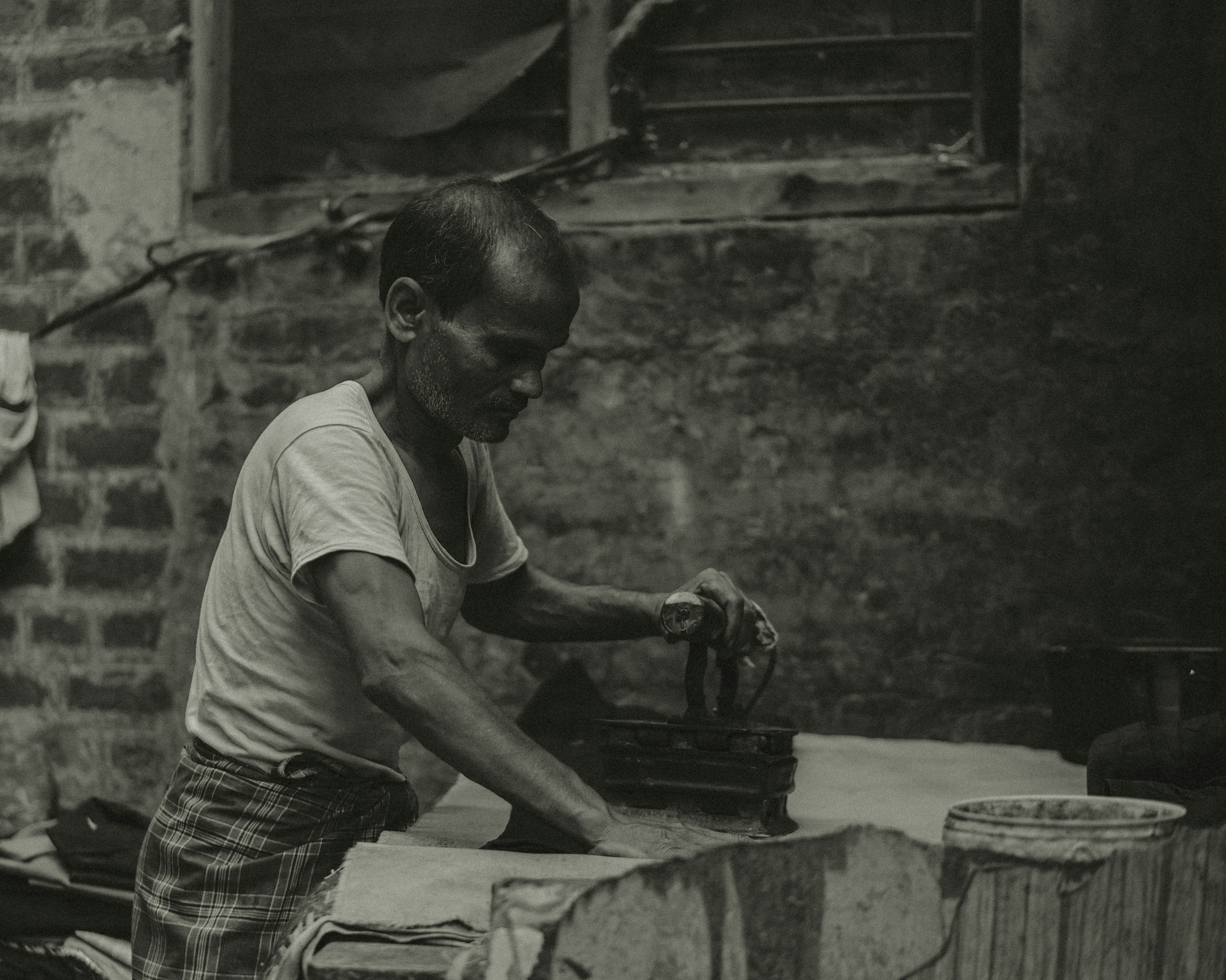 Man ironing clothes against a brick wall.