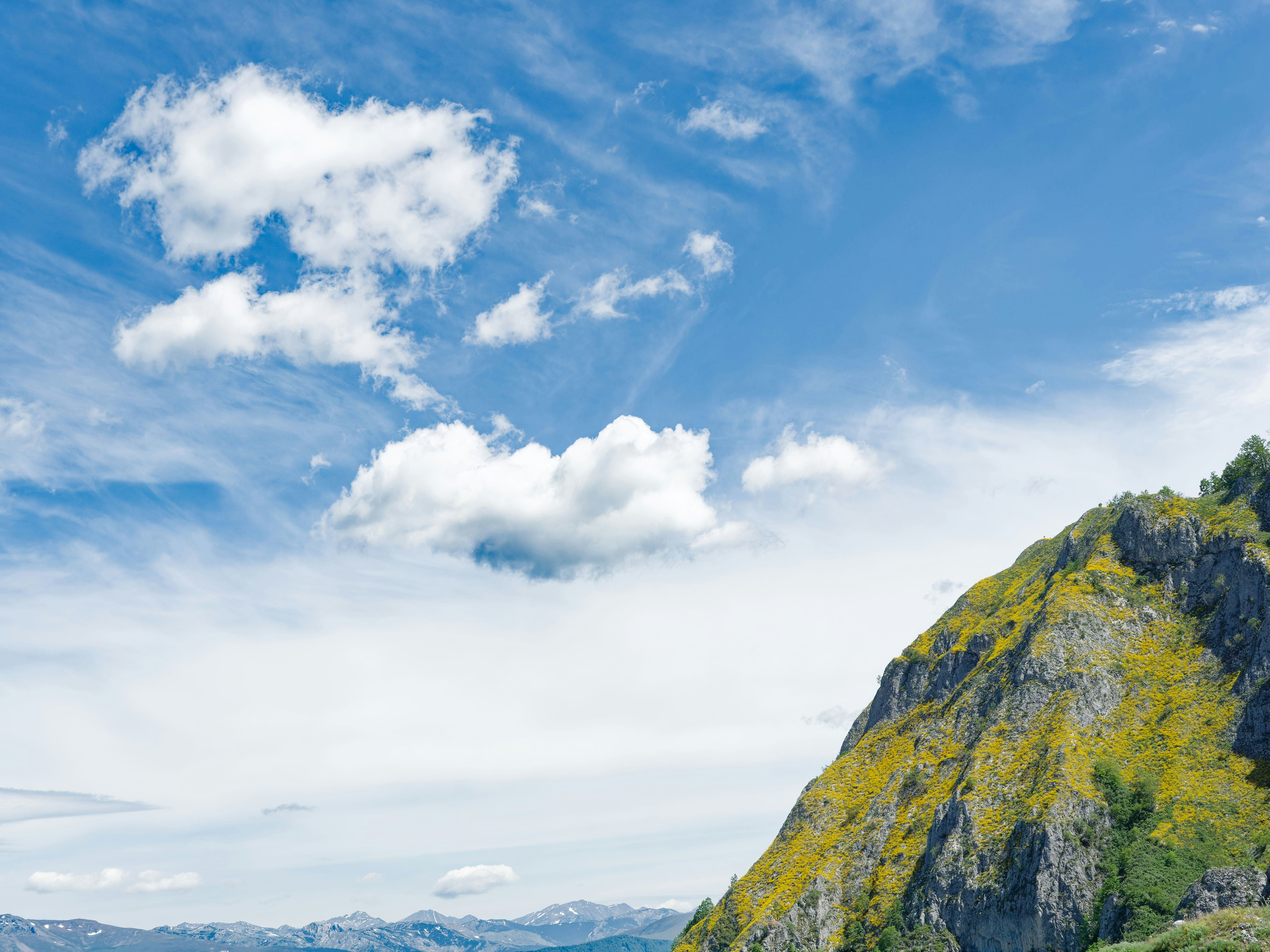 A vibrant blue sky with clouds over a green mountain.