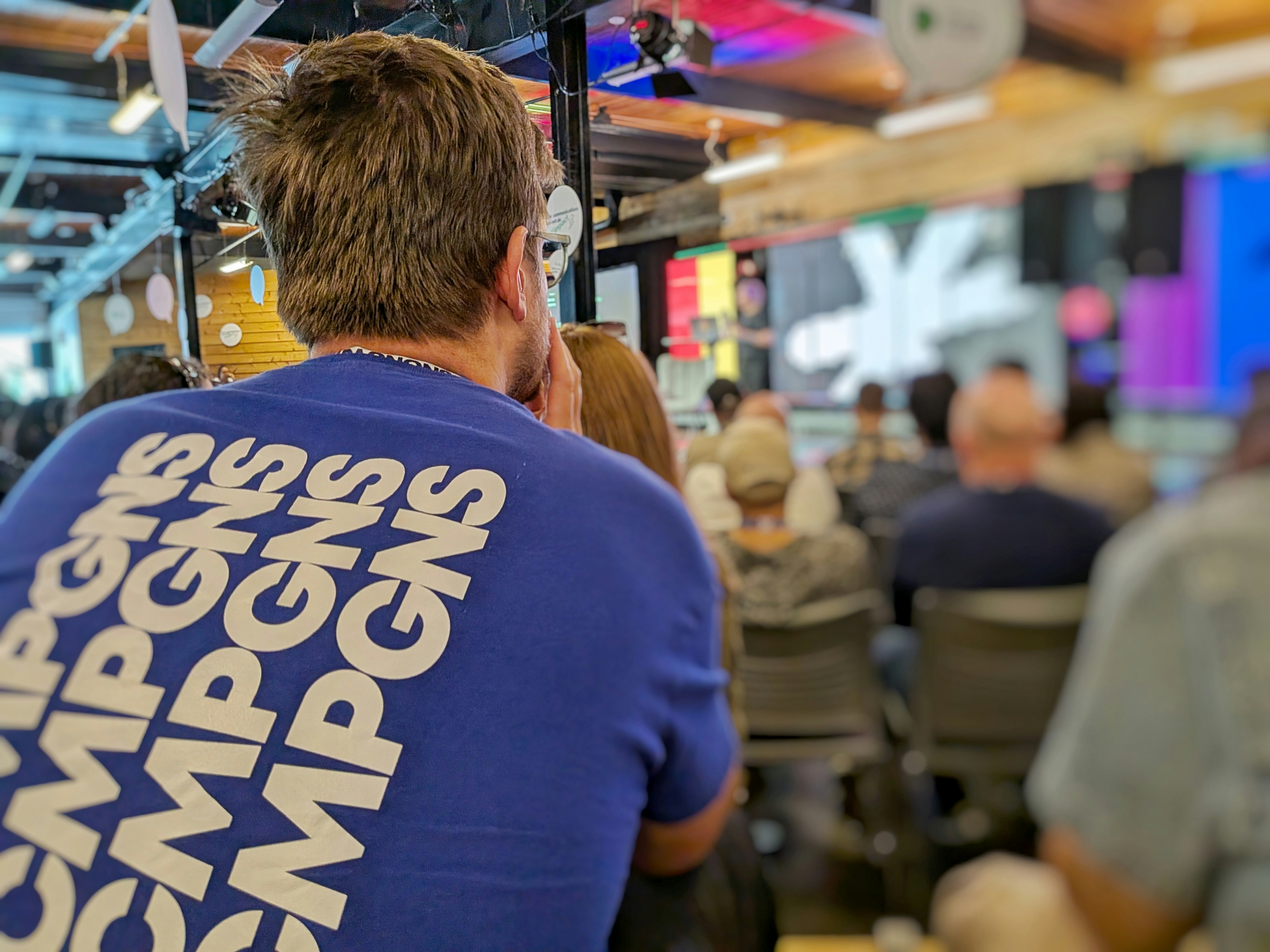 Person in blue "cmpgns" shirt attending an indoor event.
