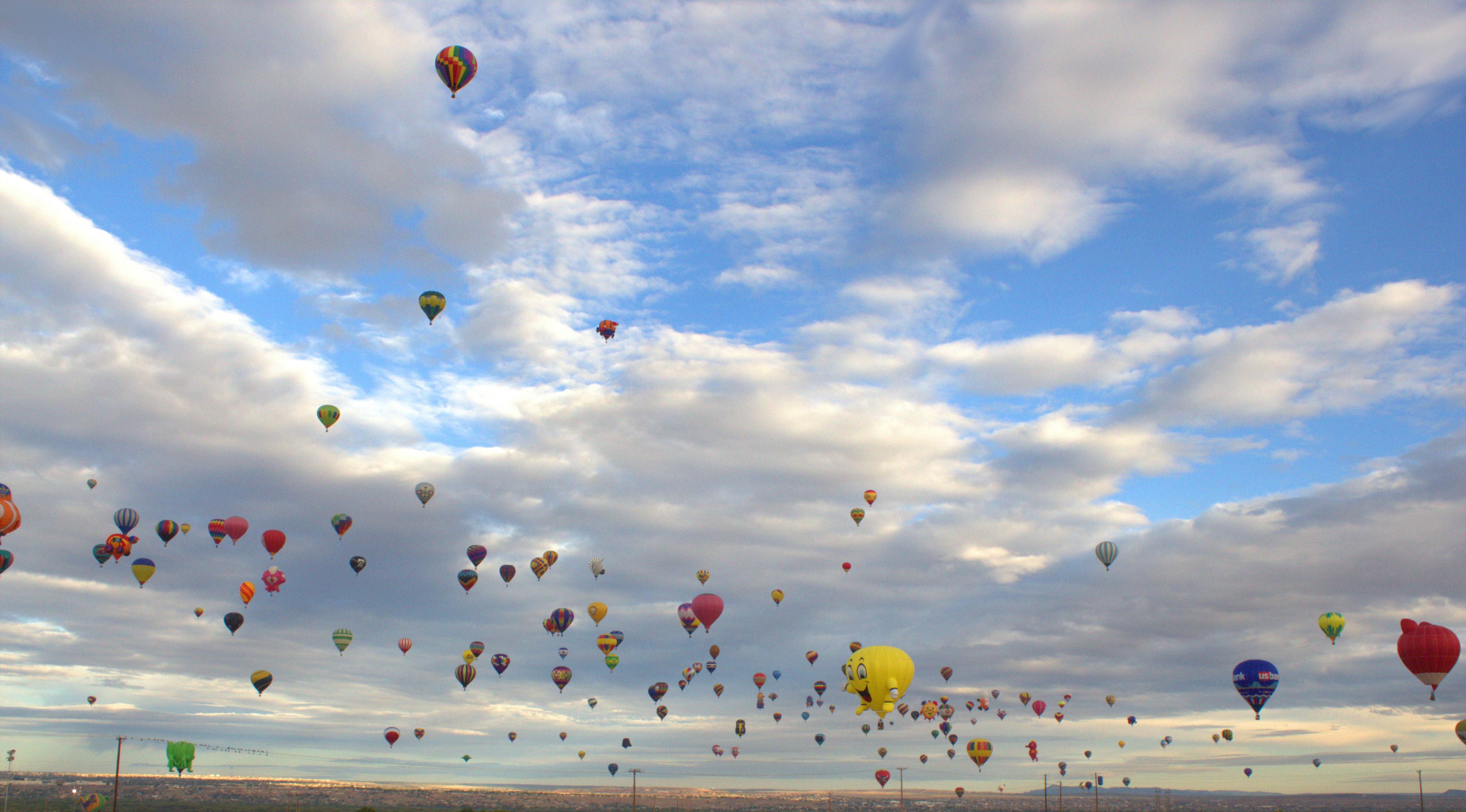 Vast horizon filled with colorful hot air balloons drifting across a bright sky with scattered clouds.