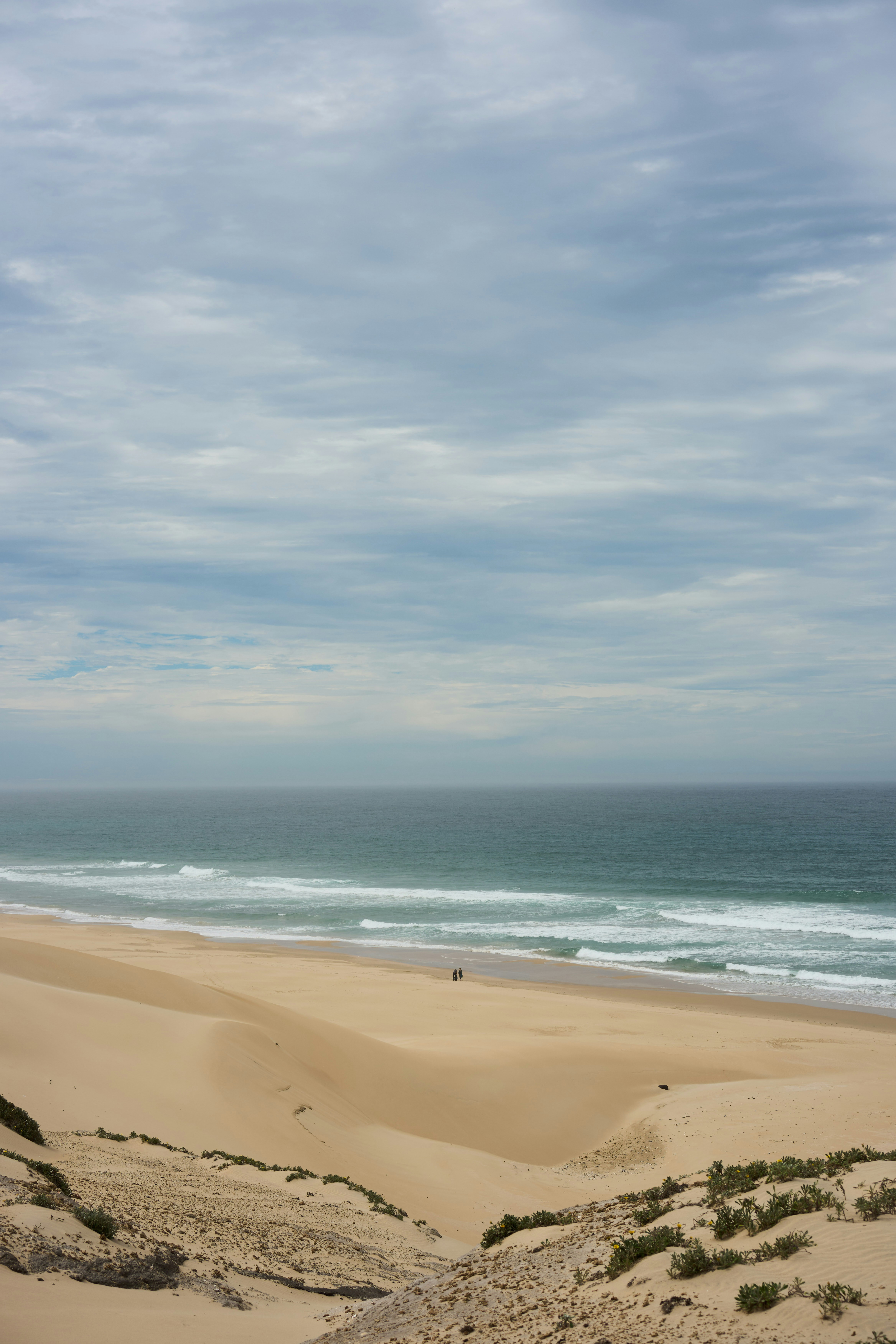 Vast sandy beach with ocean waves and cloudy sky.