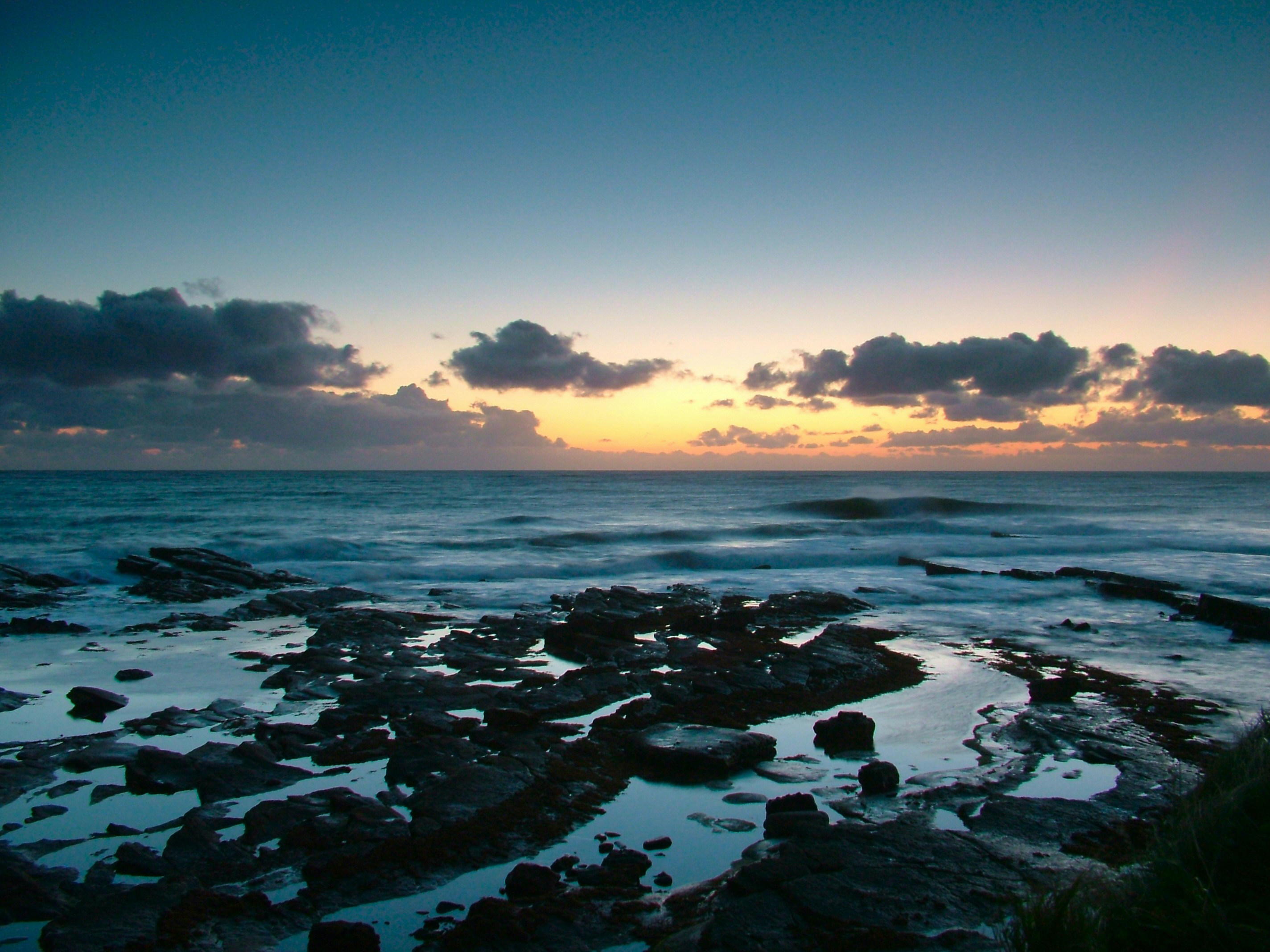 Sunset Over Rocky Shoreline: Quiet Waves Meeting the Horizon