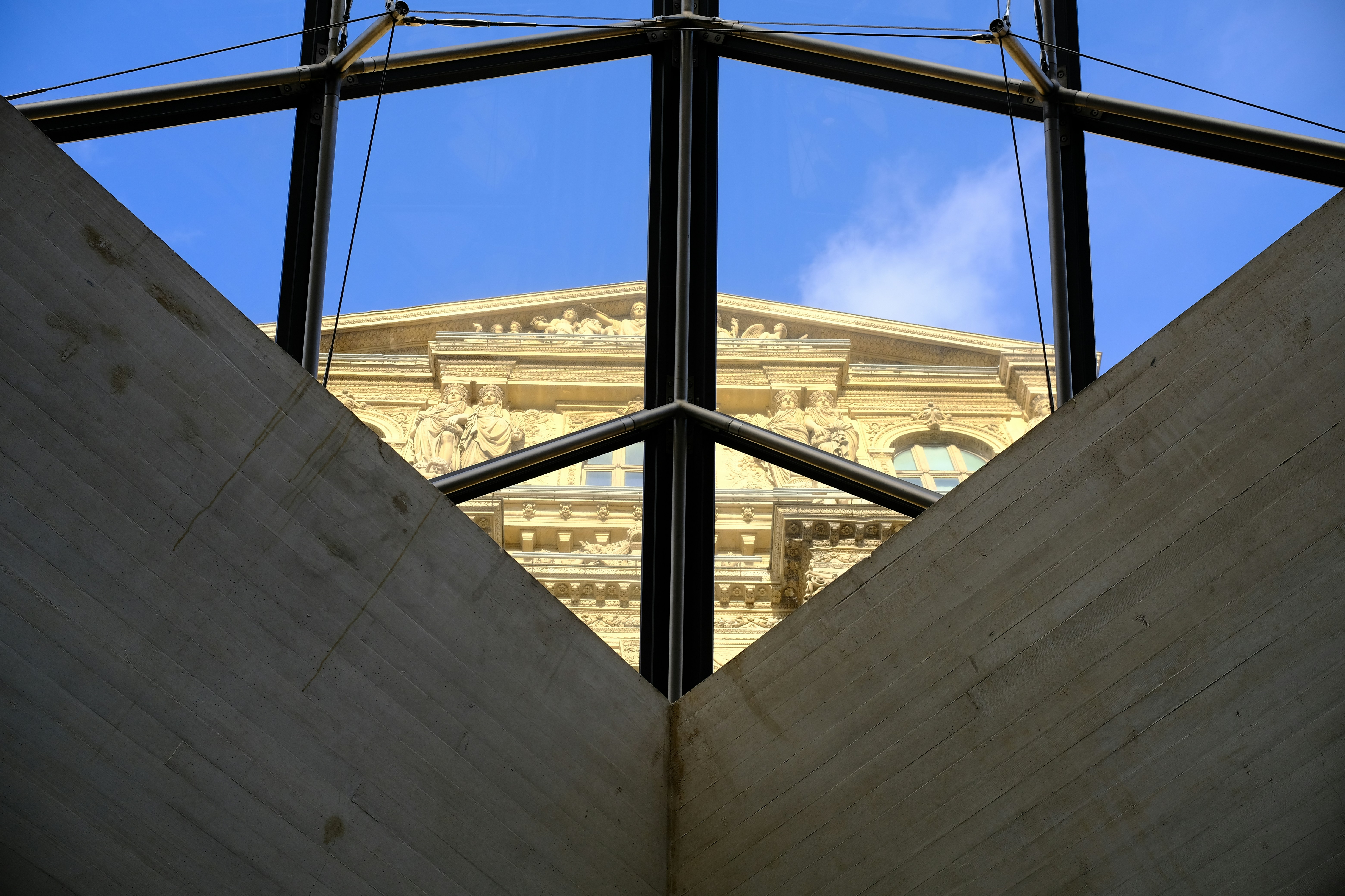 Ornate building reflected in glass, framed by modern architecture.