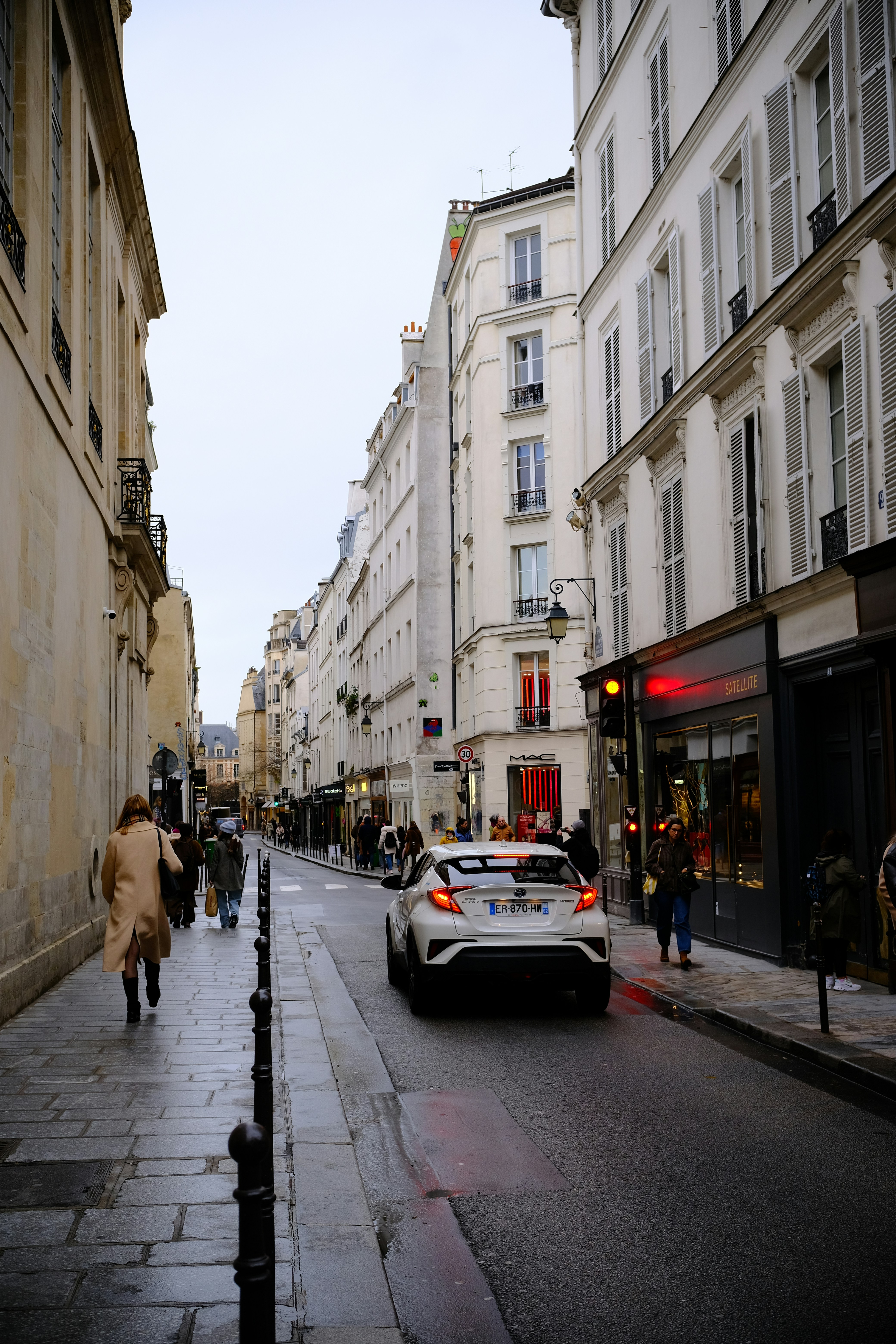 City Street in Paris: White Car and Passersby Amid Historic Facades