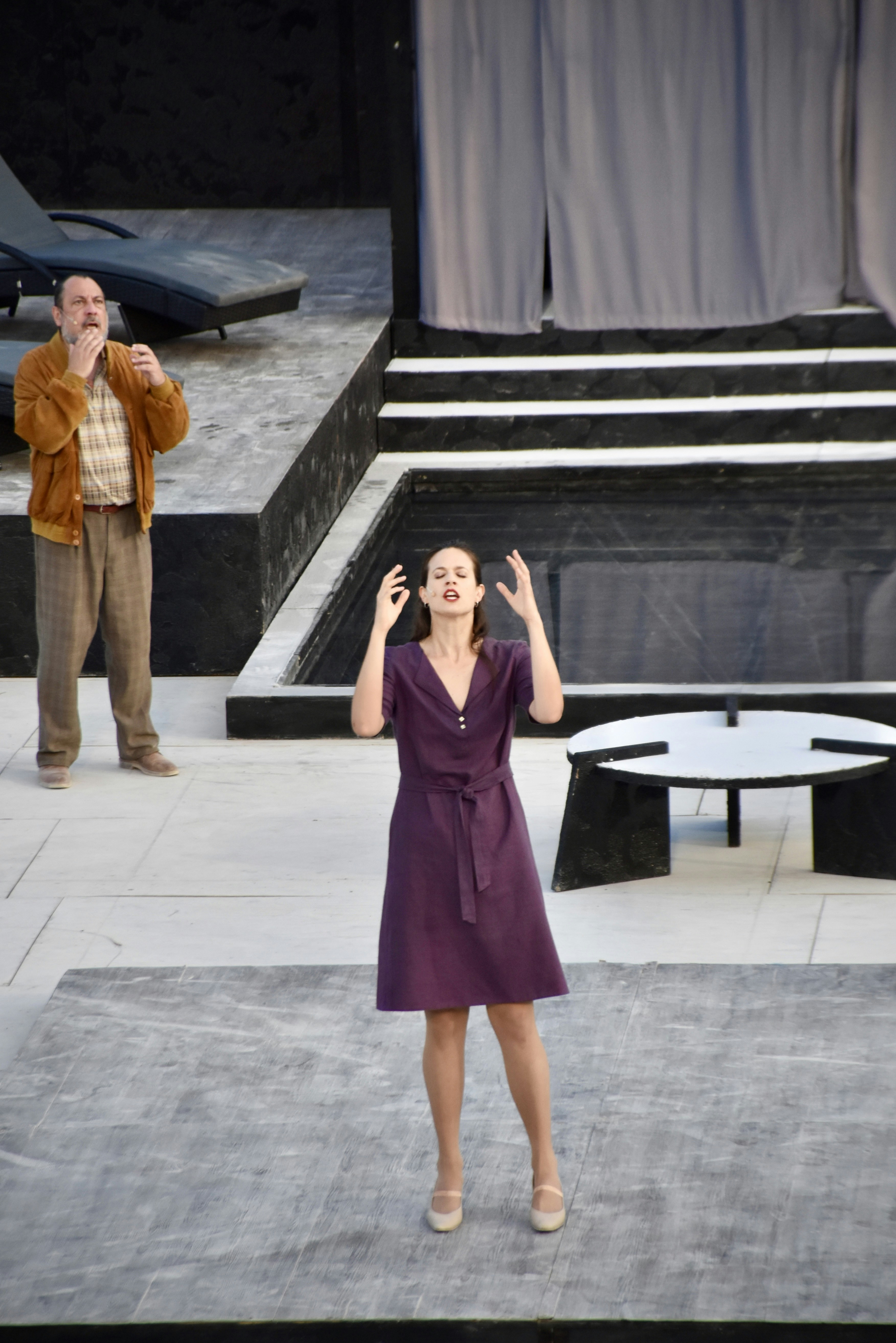 Purple-dressed vocalist center stage with a backdrop of a sunken circular pool and two observers