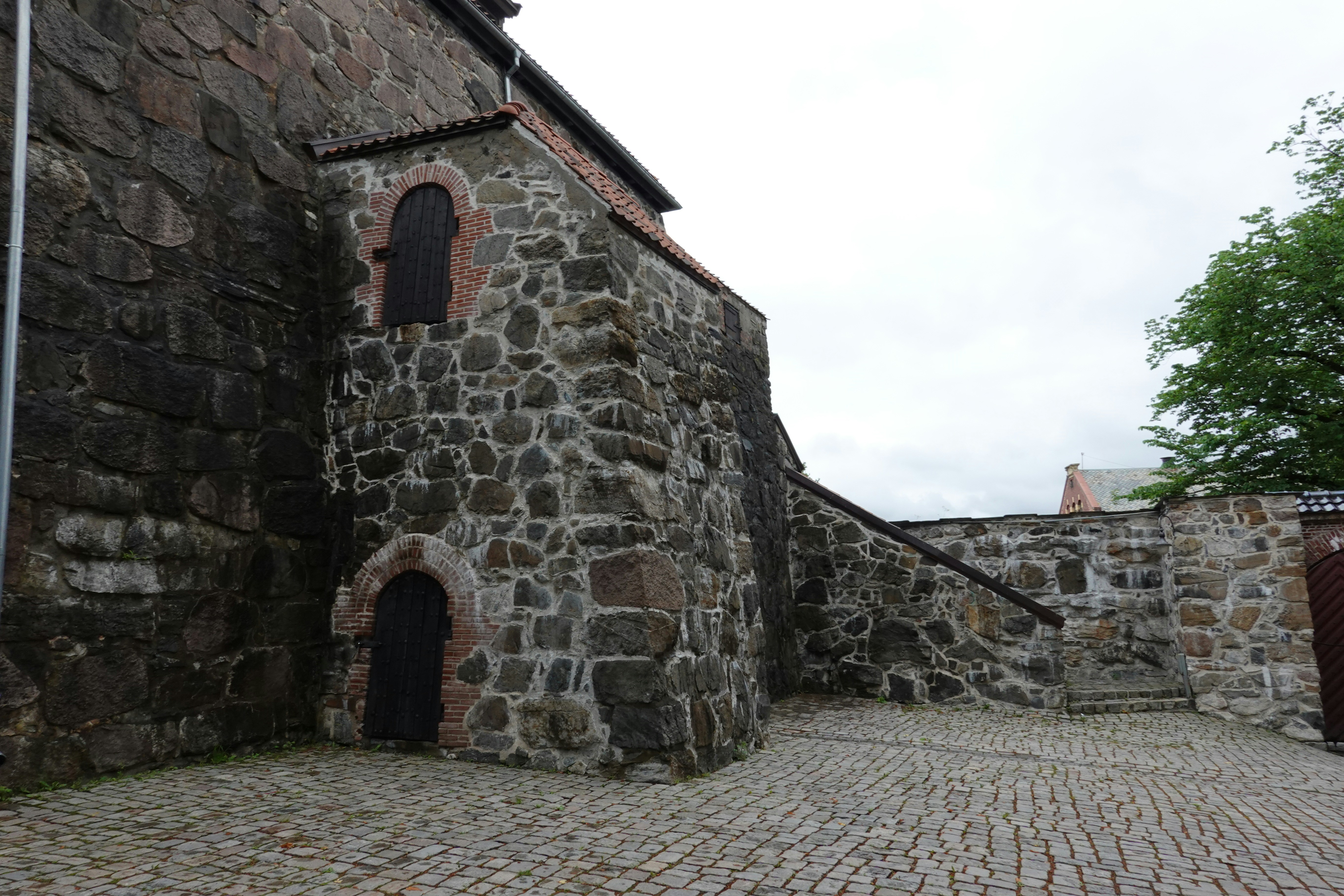 Old stone building with arched windows and cobblestone ground.