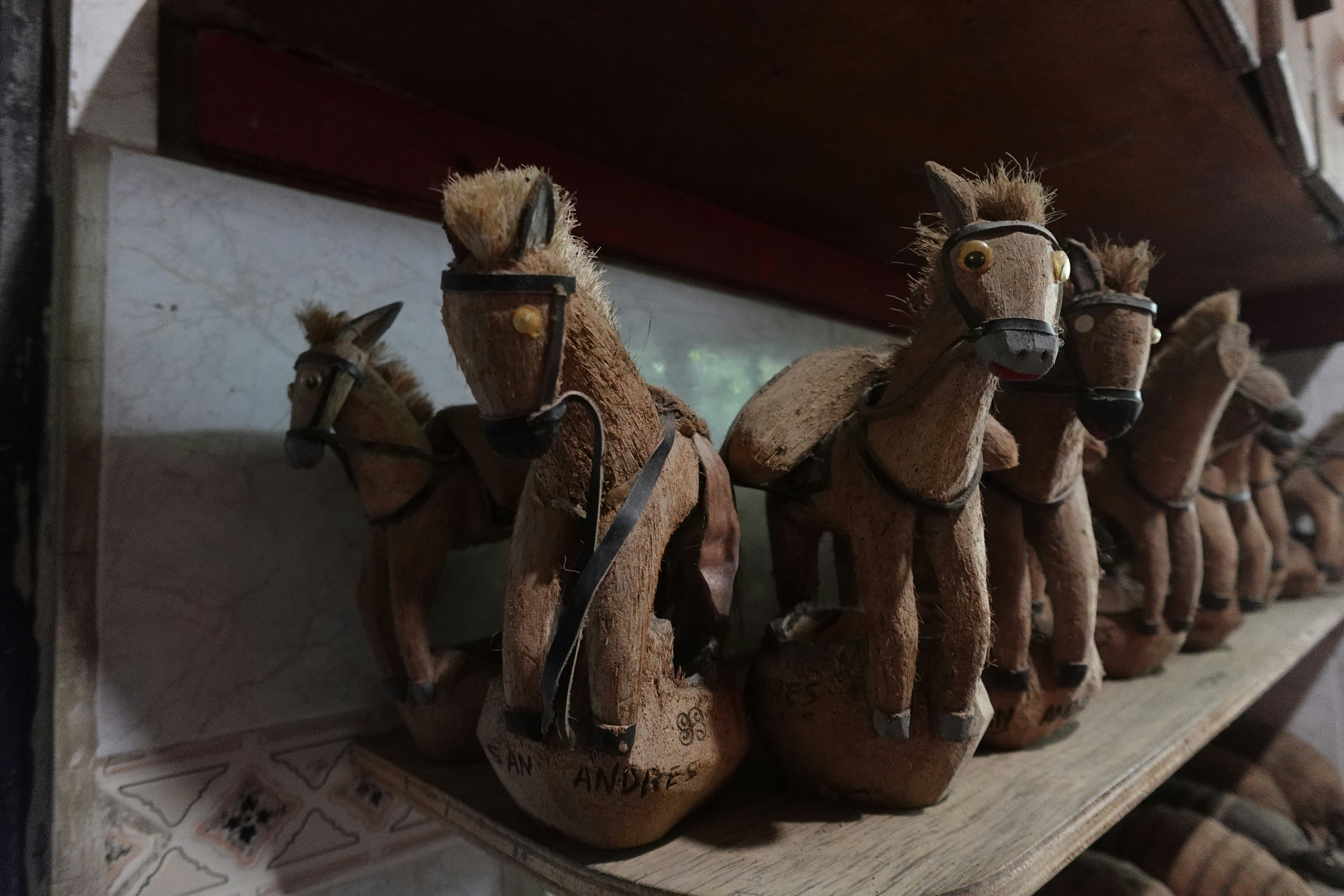 Row of carved wooden horses with bridle, lined on a shelf inside a cabinet.