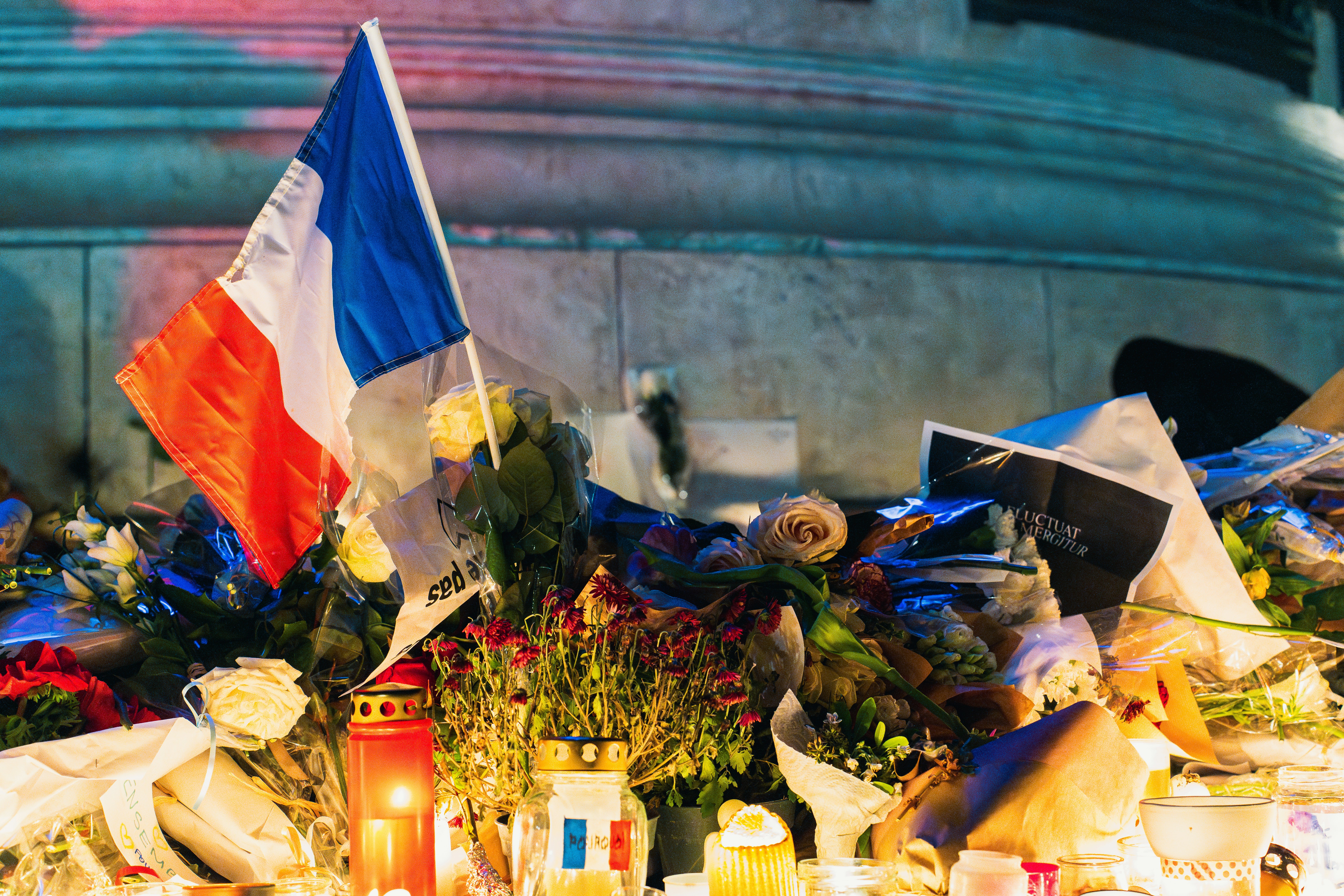 Candles, flowers, and a French flag at a vigil in front of a stone monument