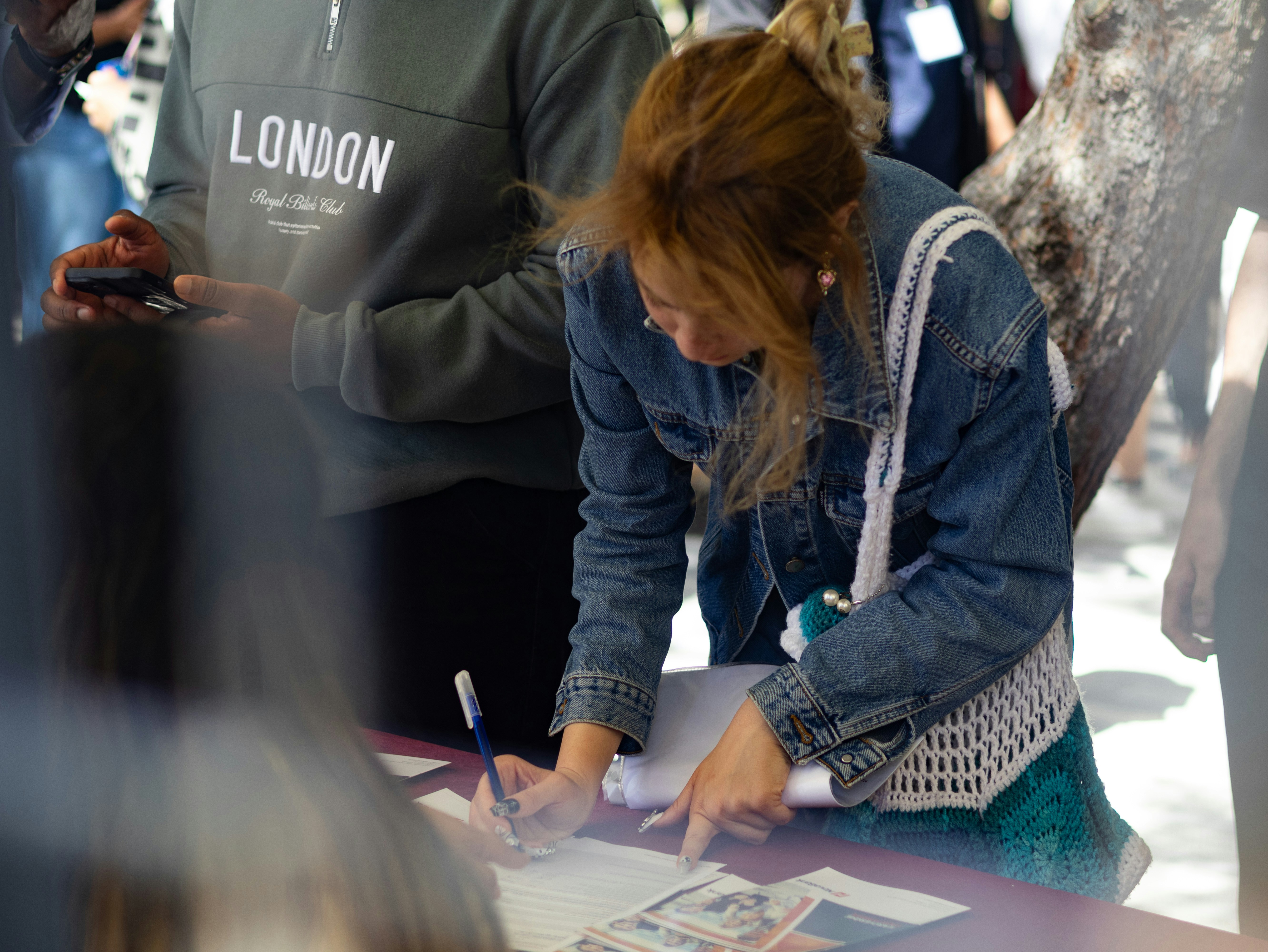 A woman signs a document at an outdoor event.