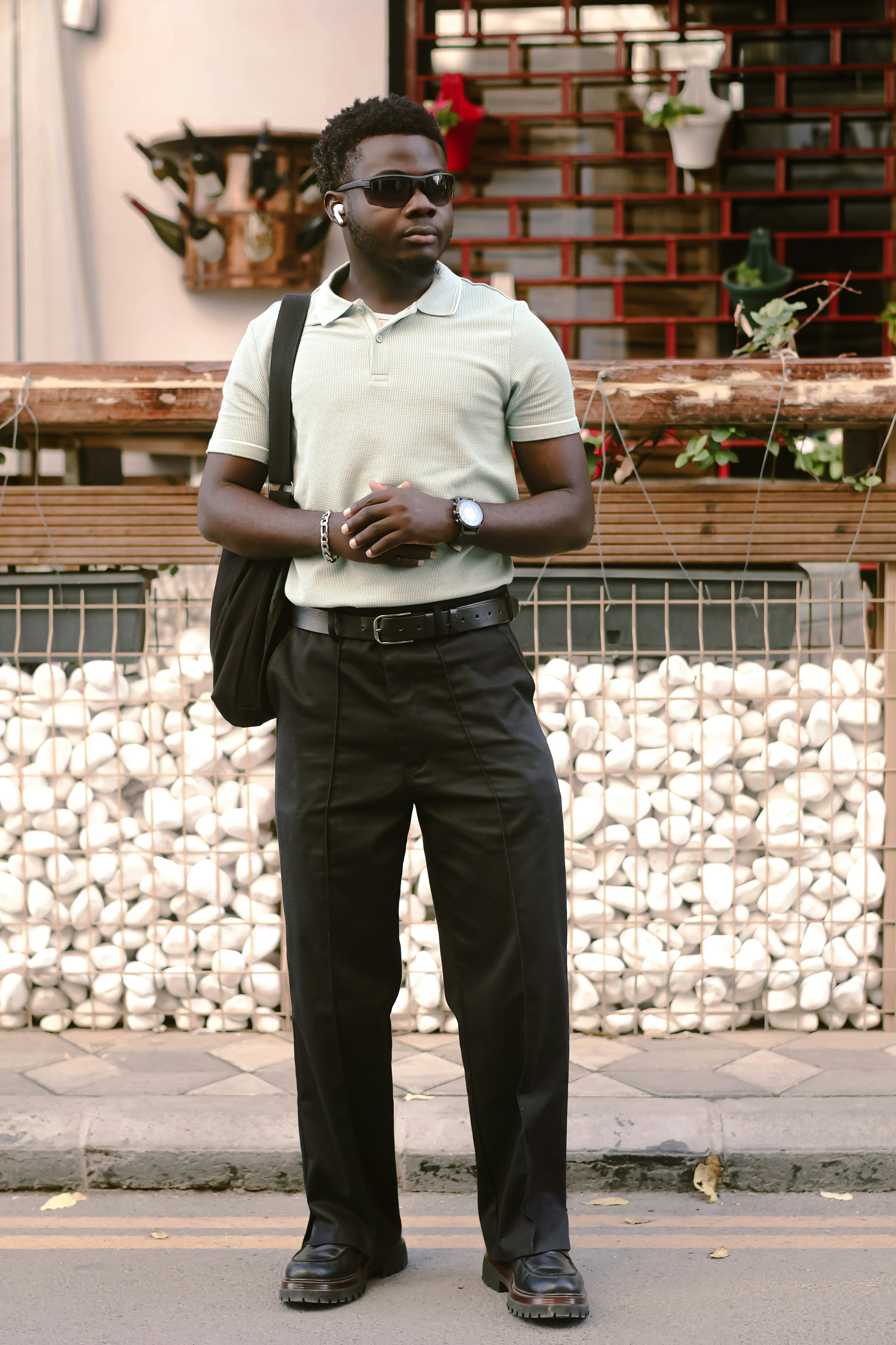 A man stands on a street with sunglasses and earbuds.