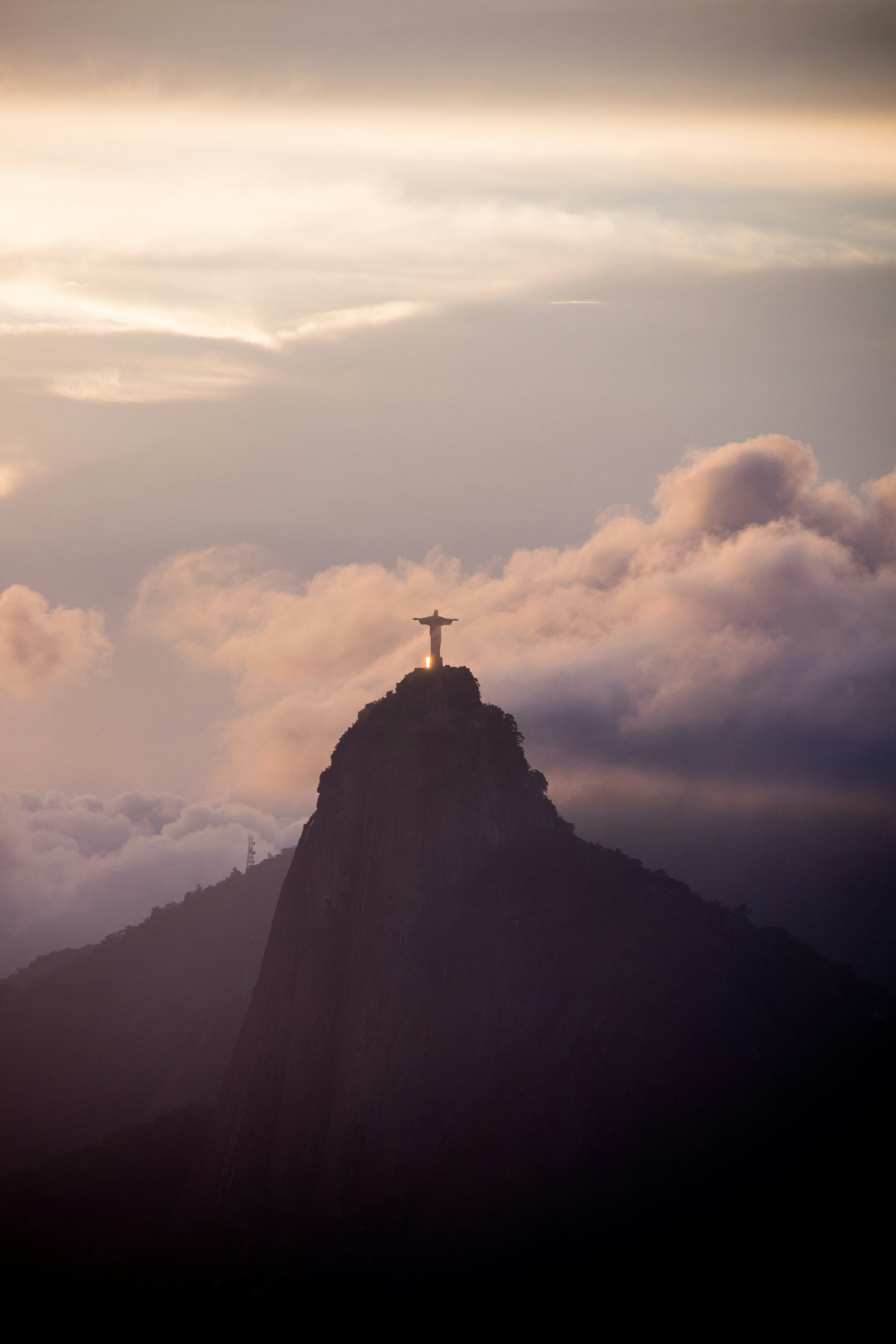 Christ the redeemer statue on a mountain peak at sunset.