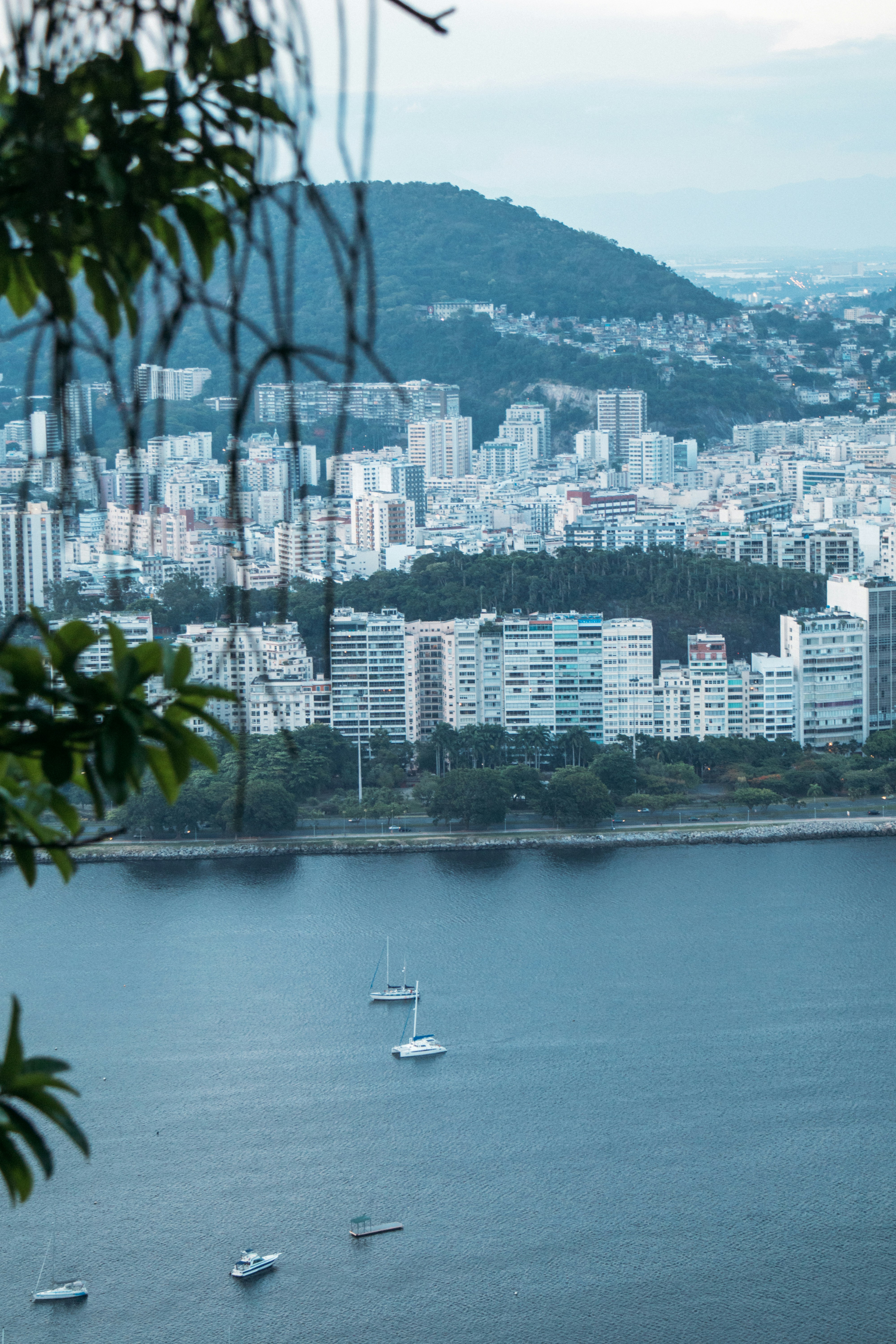 Cityscape overlooking water with boats and a distant mountain.
